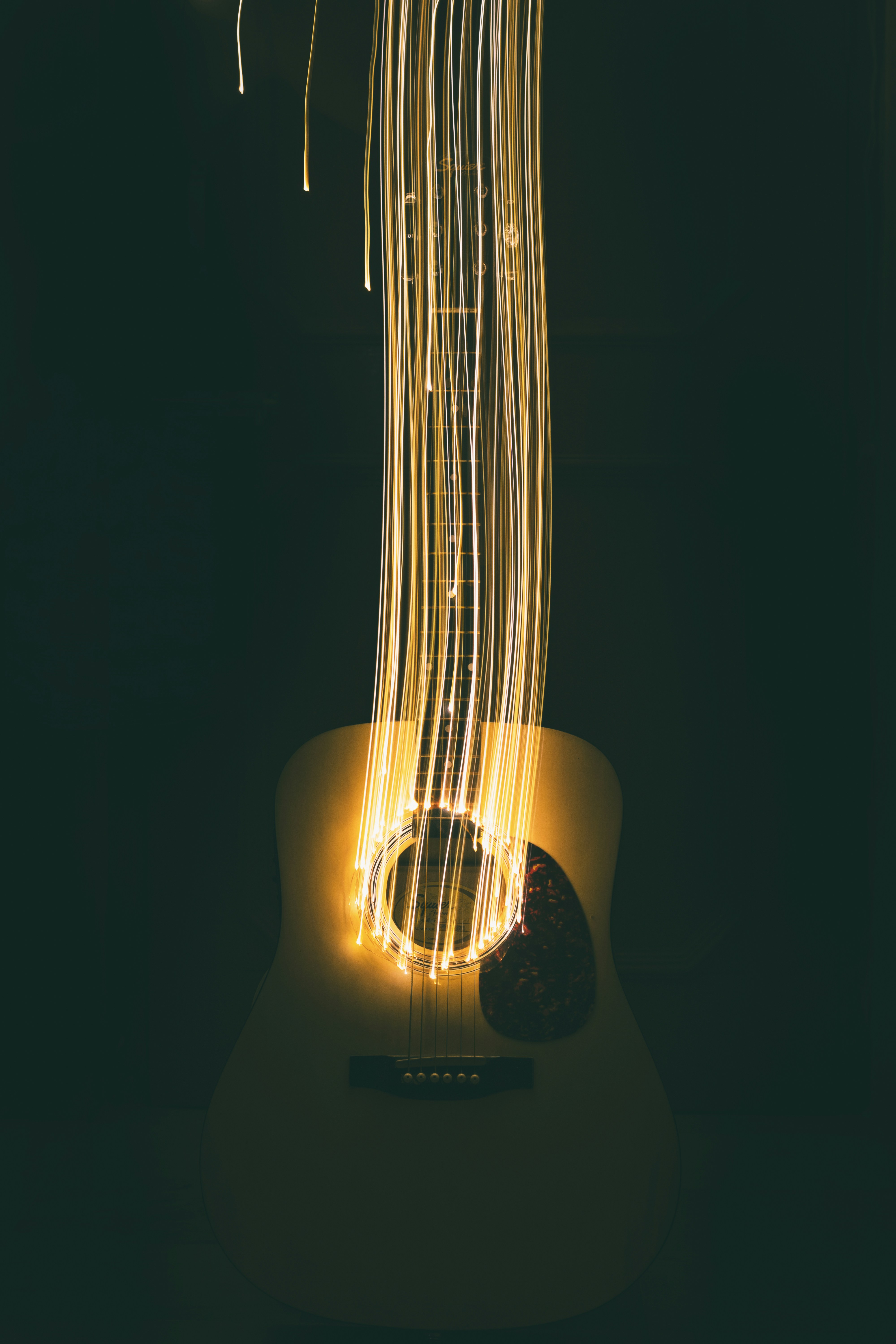 An illuminated acoustic guitar with swirling light trails creating a dynamic visual effect in a dark setting.
