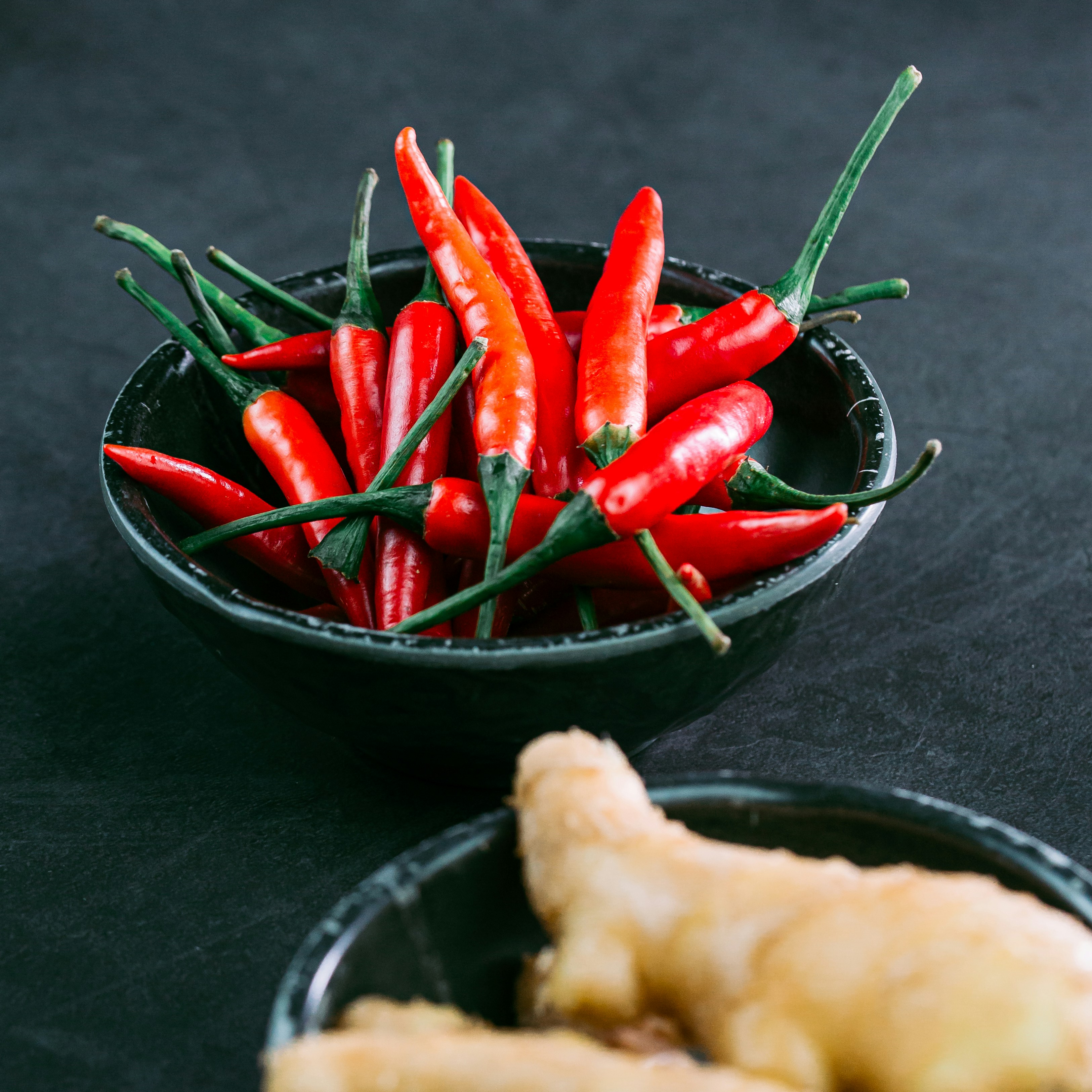 Vibrant red and green chilies arranged in a black bowl, accompanied by golden fried chicken pieces. 