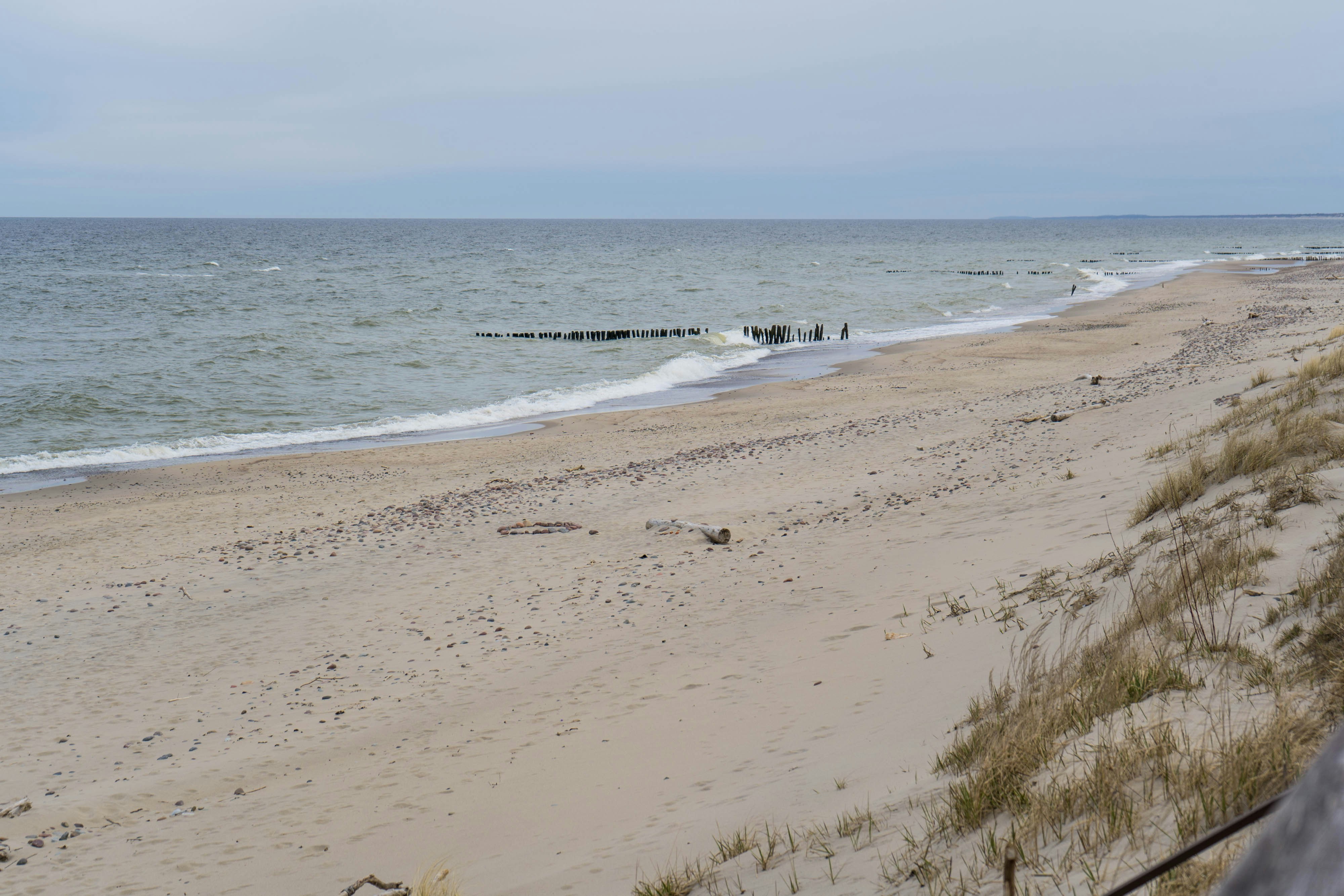 Expansive sandy beach with gentle waves meeting the shoreline under a muted sky.