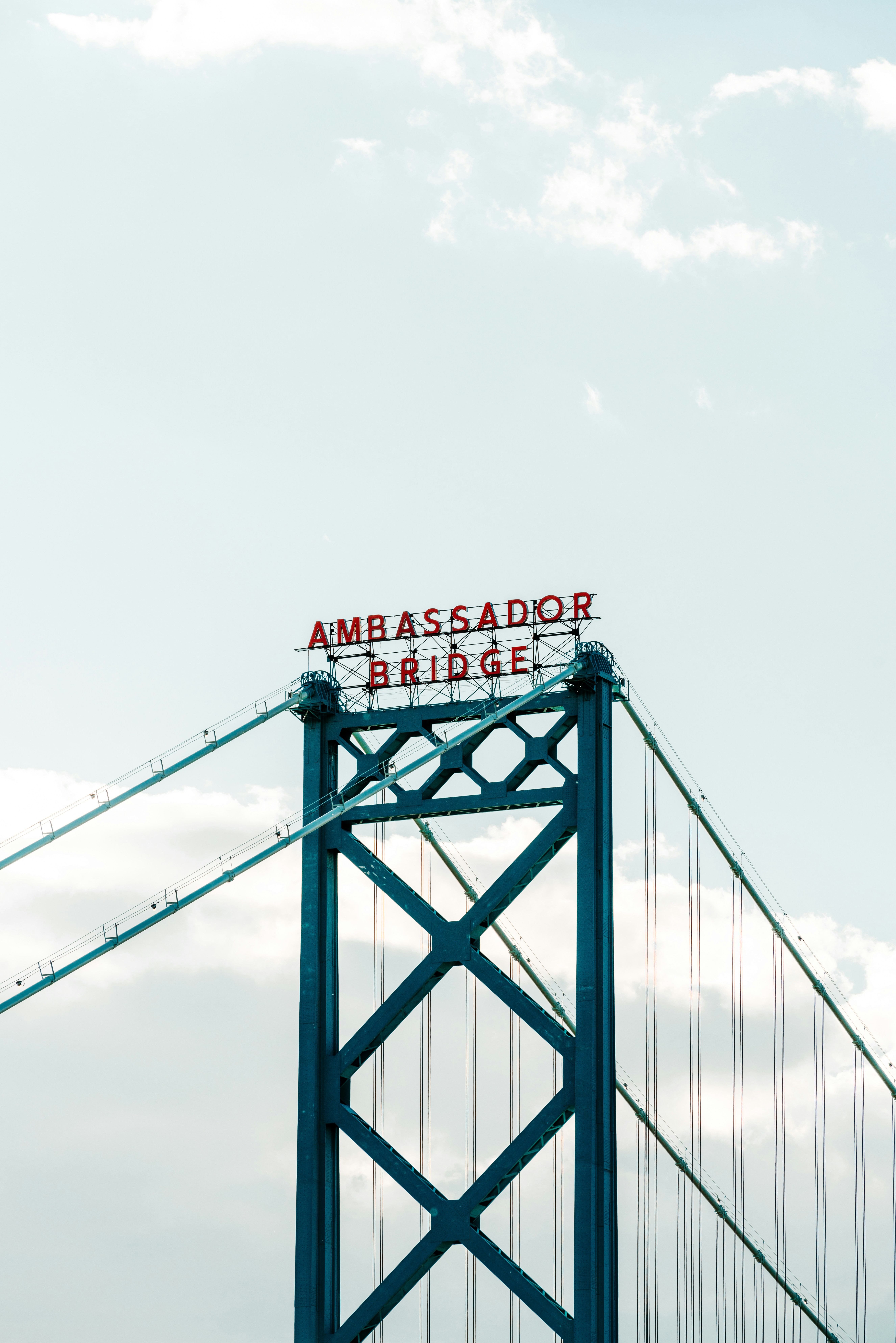 The Ambassador Bridge stands tall with its iconic red lettering against a pale sky, showcasing its structural beauty and significance as a cross-border link.