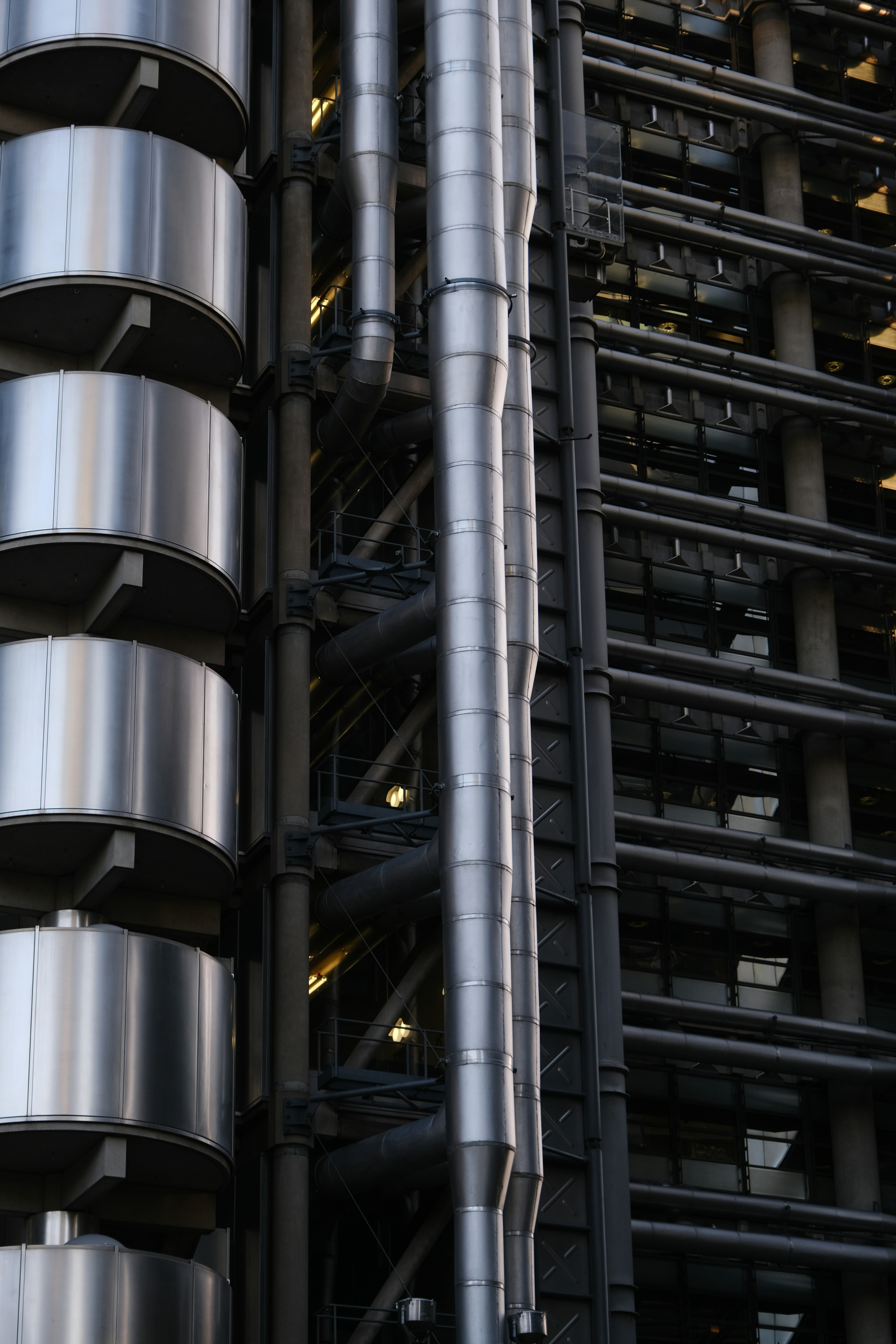 Close-up of a metallic building facade showcasing intricate piping and cylindrical structures. The design emphasizes the blend of functionality and aesthetic appeal.