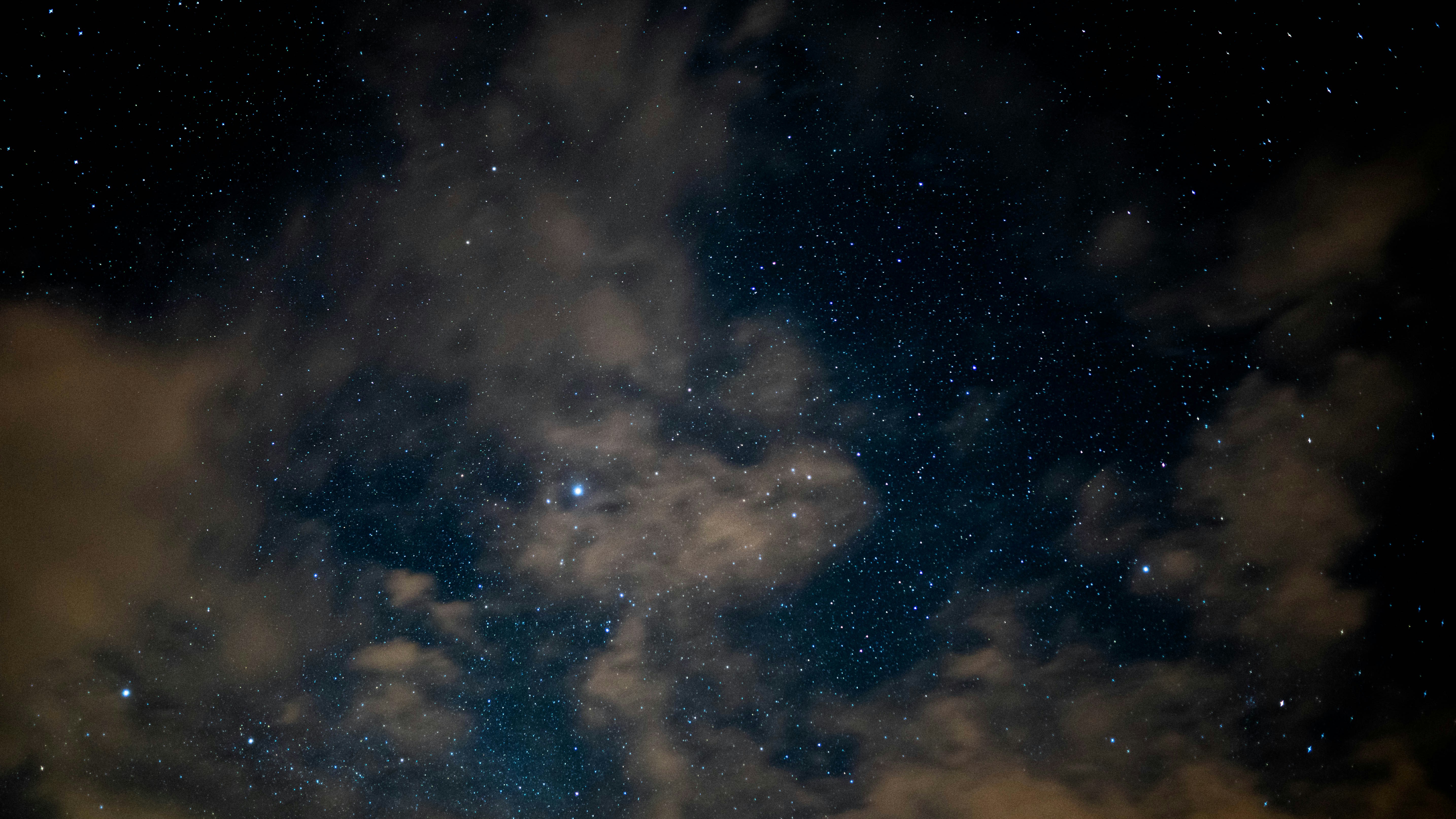 Vast expanse of stars twinkling through wispy clouds against a deep blue backdrop, showcasing the beauty of the night sky.
