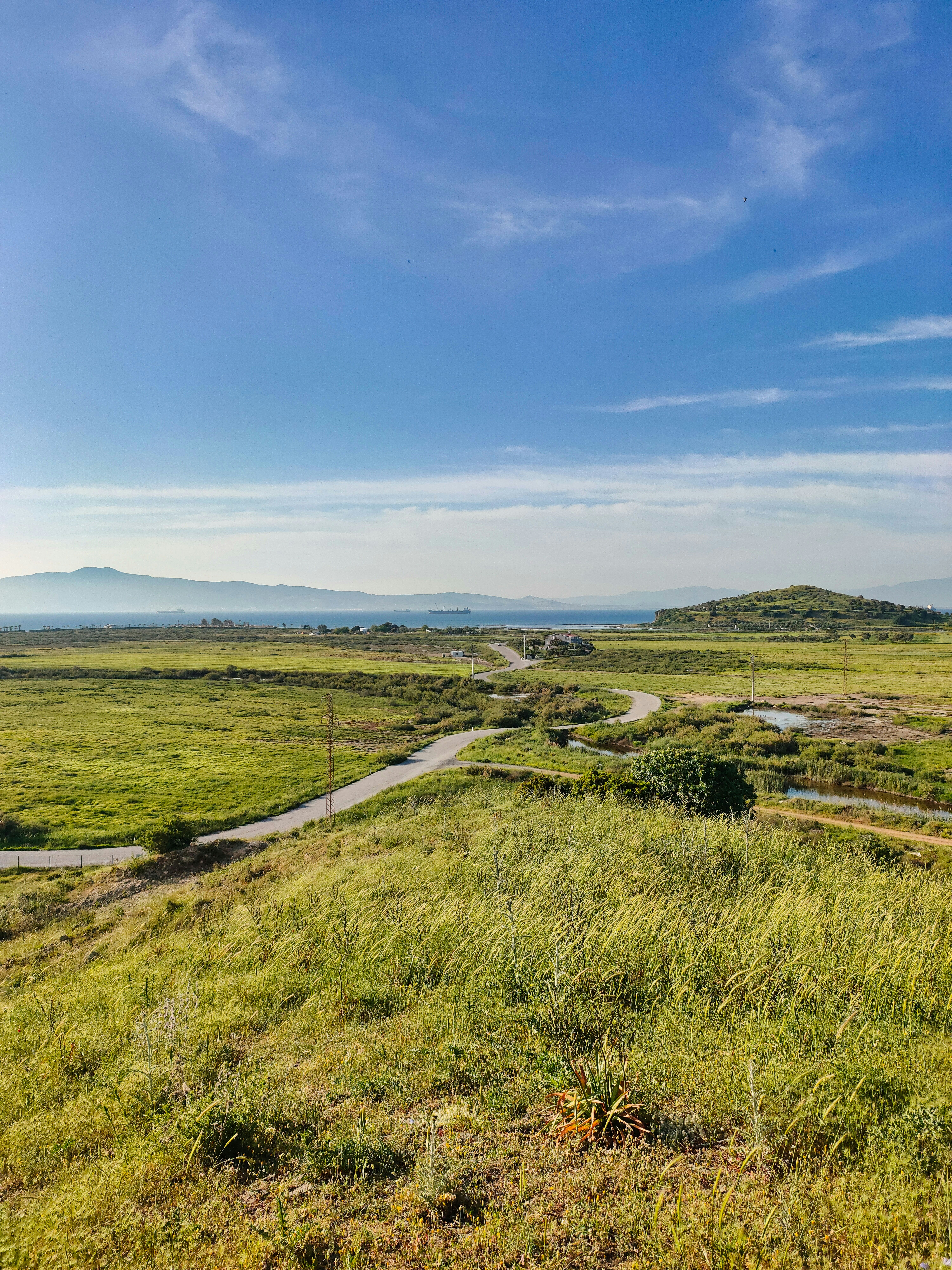 Sunlit coastal plain photograph with a winding road leading toward the distant sea under a clear blue sky.