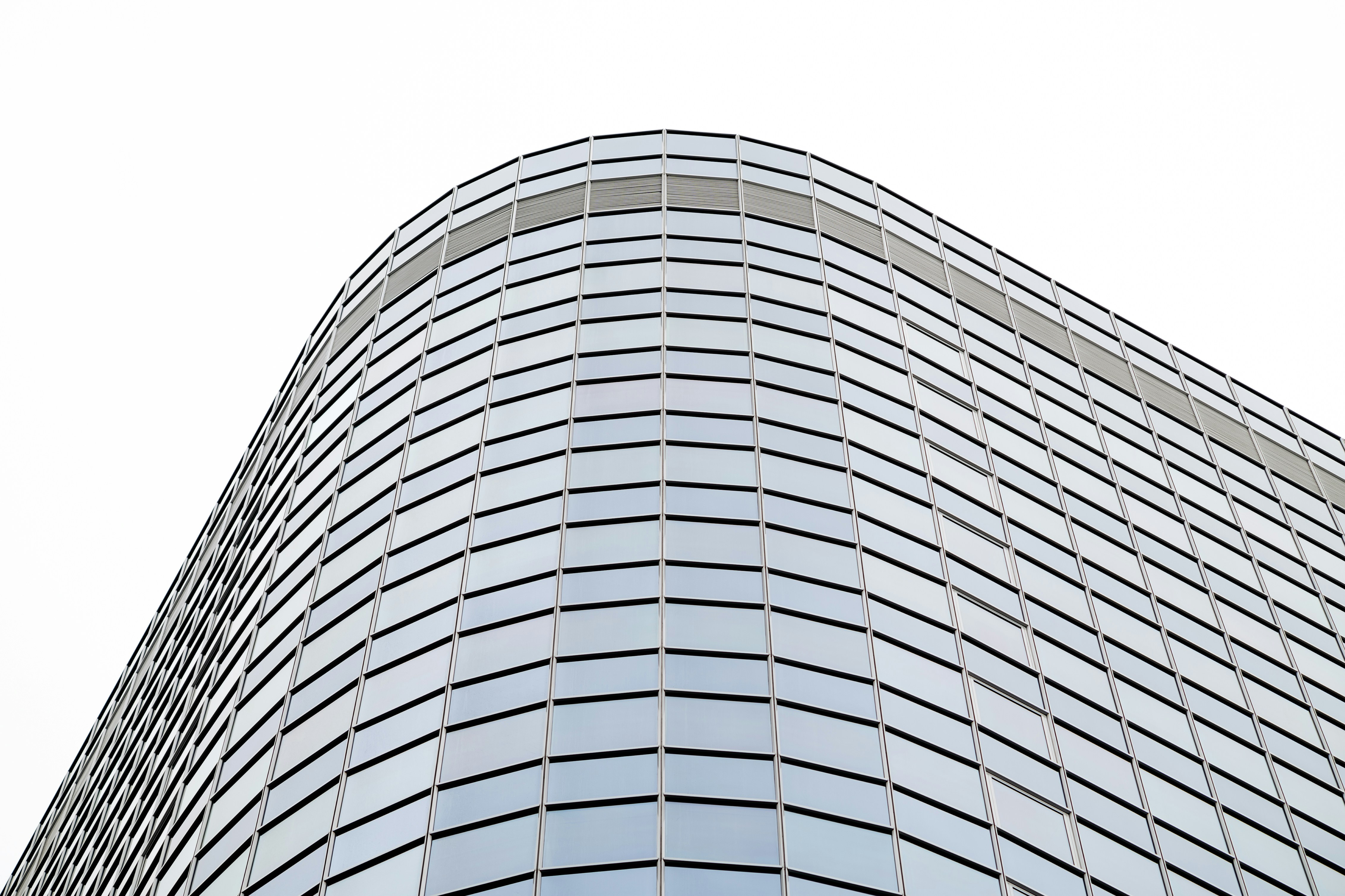 Modern building facade showcasing a sleek, curved design with reflective glass panels. The minimalist aesthetic emphasizes the interplay of light and structure.