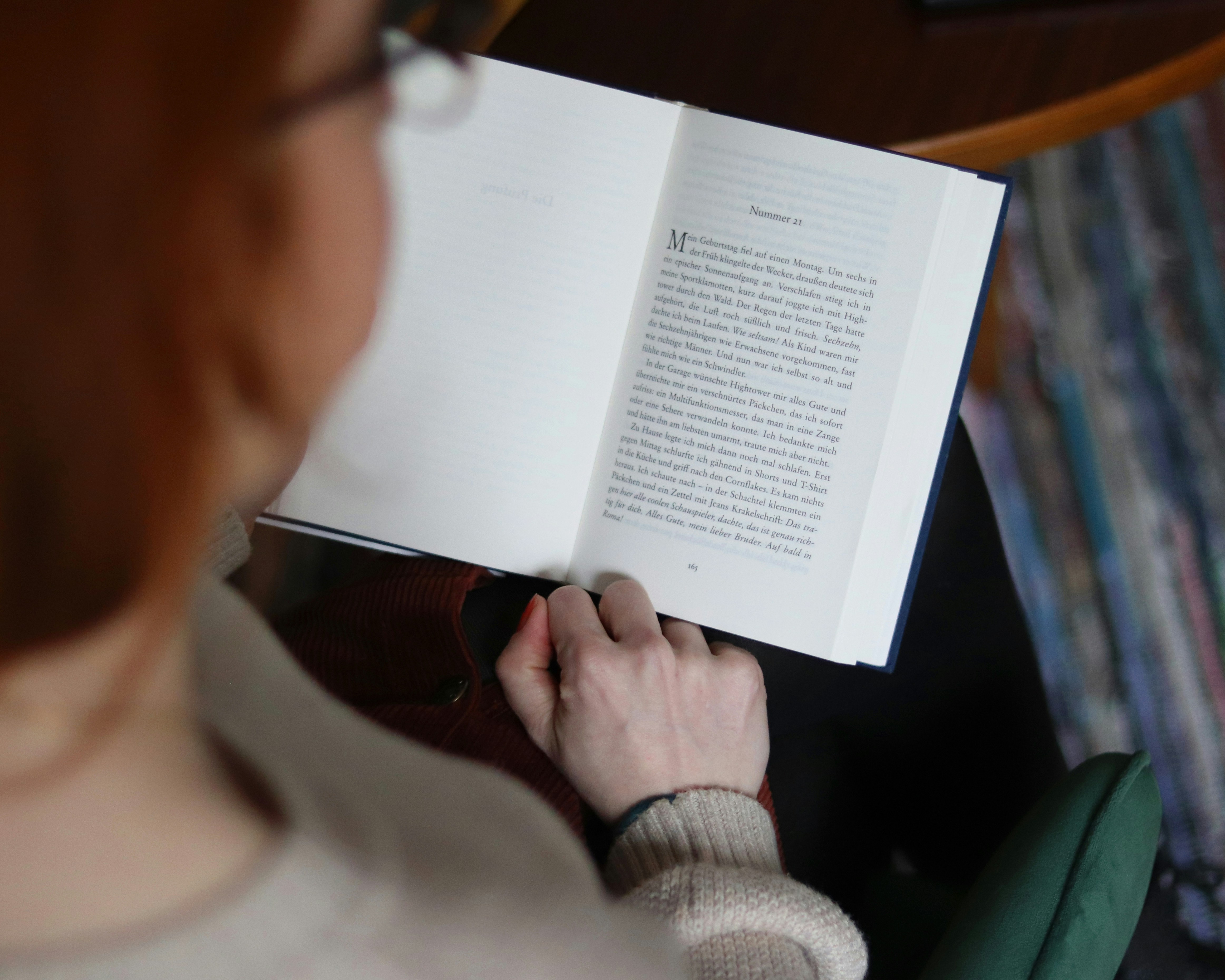 A person reading a book, their hand holding the pages, with soft focus on the text. The scene captures a moment of quiet reflection.