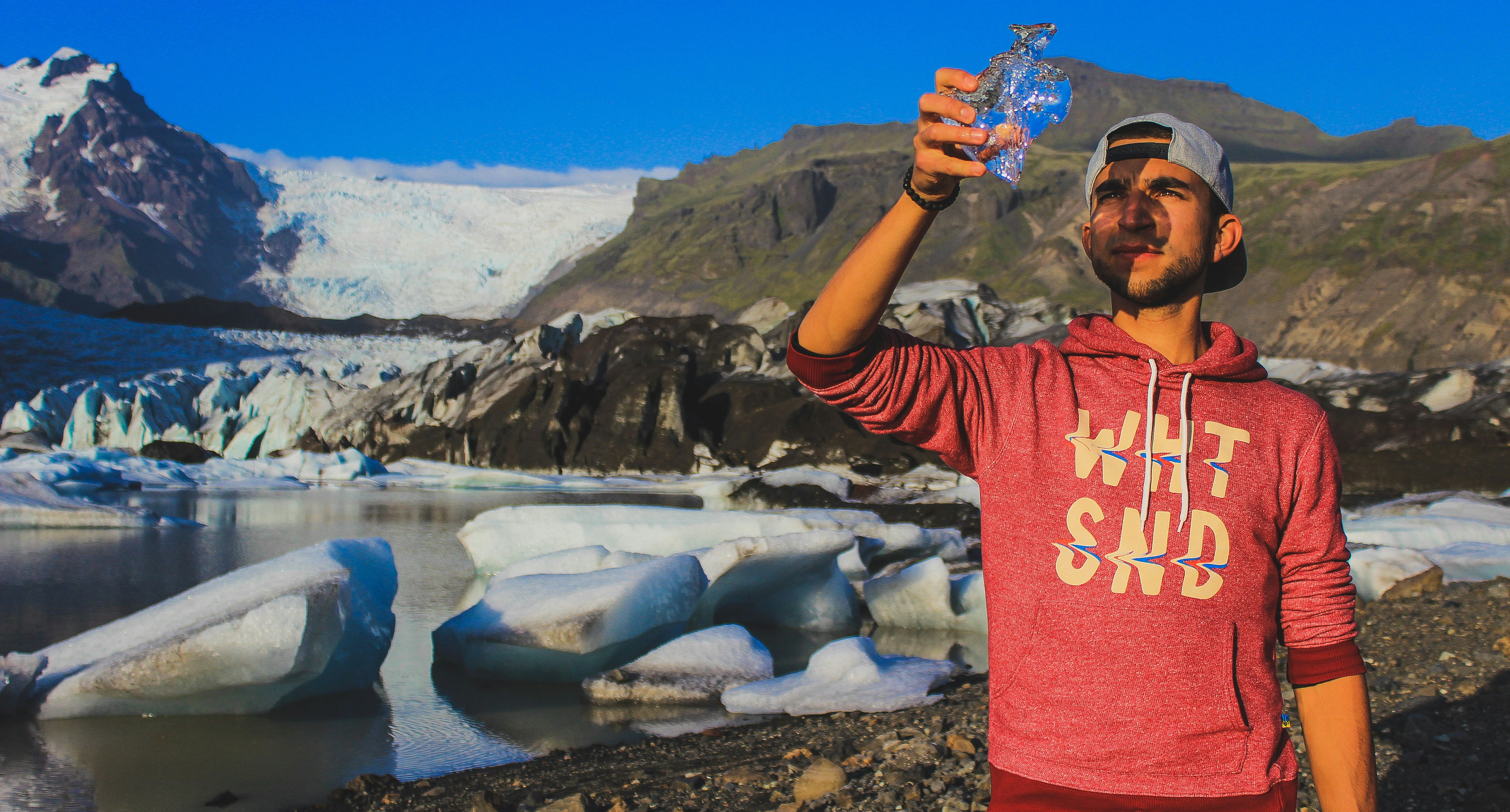 Individual holding a clear water bottle against a backdrop of a glacial landscape, showcasing the interplay of nature and human interaction.