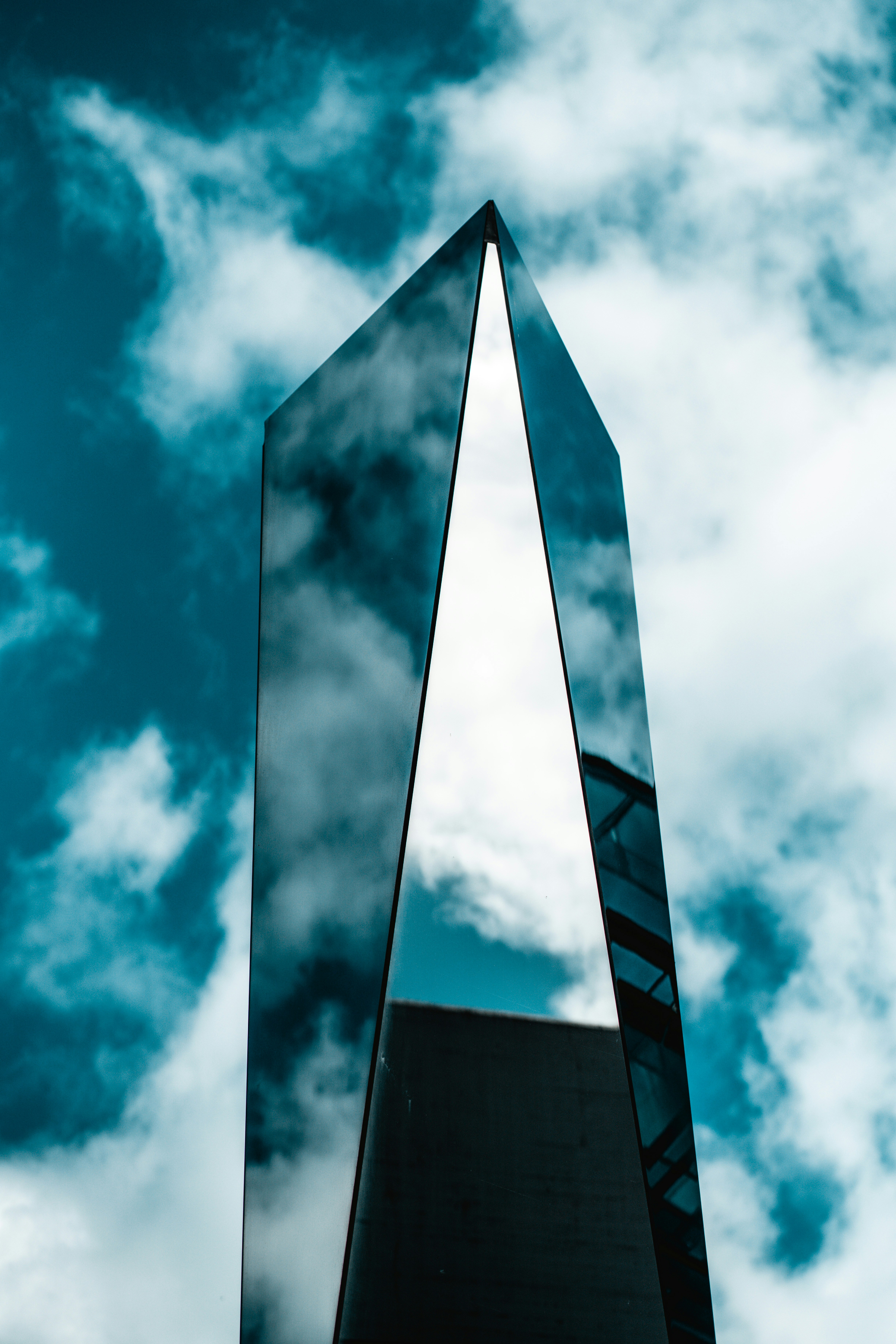 Prismatic Peak: A Glass Obelisk Piercing a Sky of Clouds