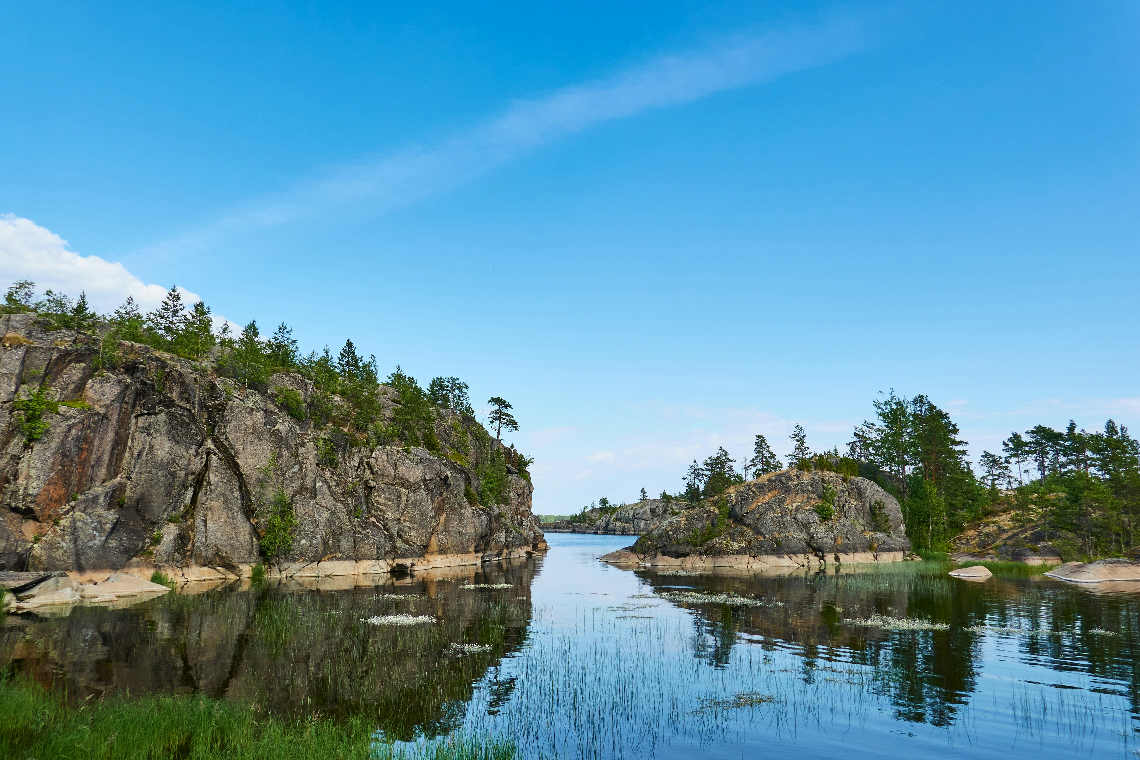 Small rocky islands on Lake Ladoga reflecting in calm waters under a clear blue sky.