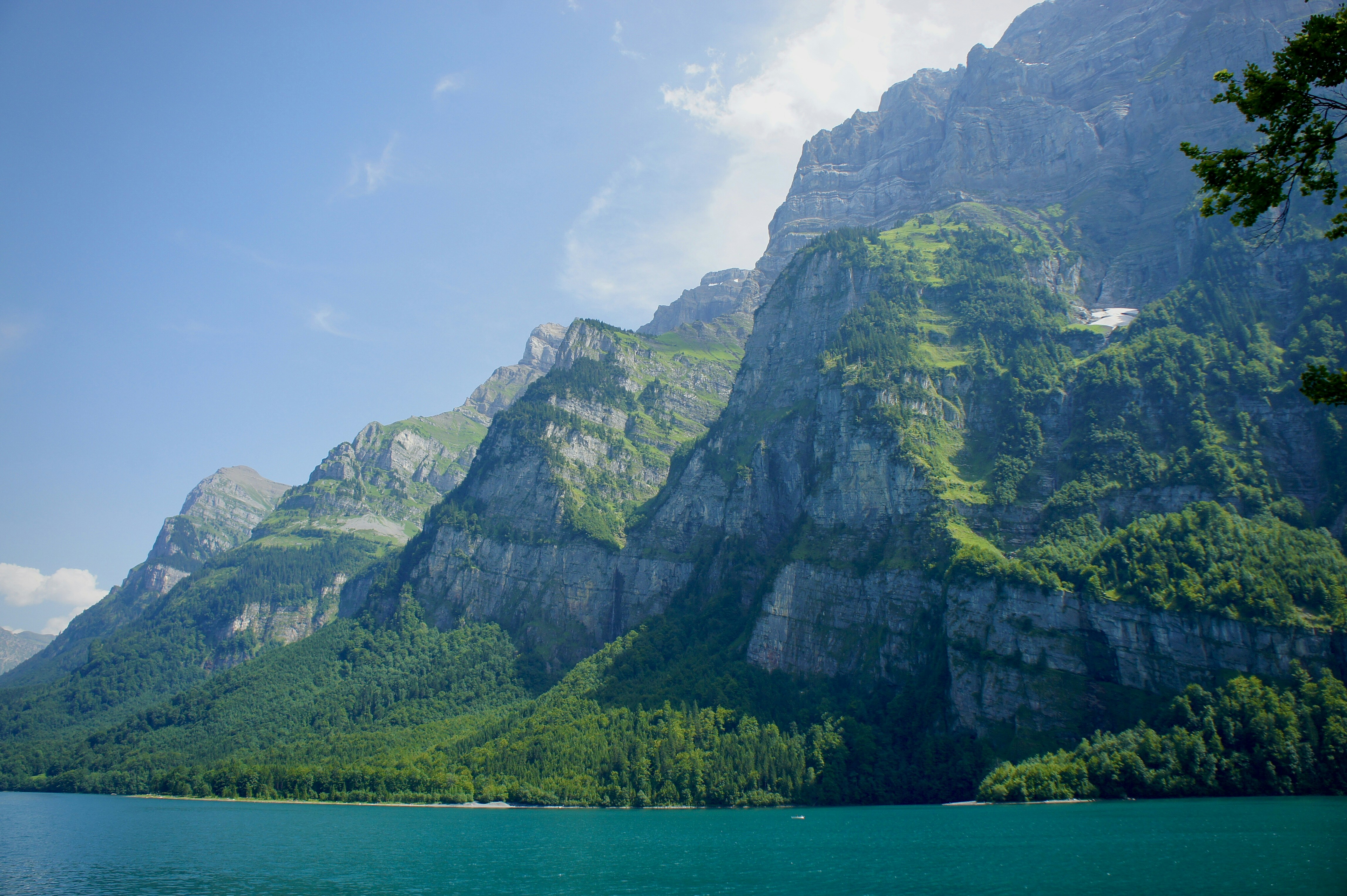 Towering mountains with lush greenery rise above a tranquil turquoise lake under a clear blue sky.