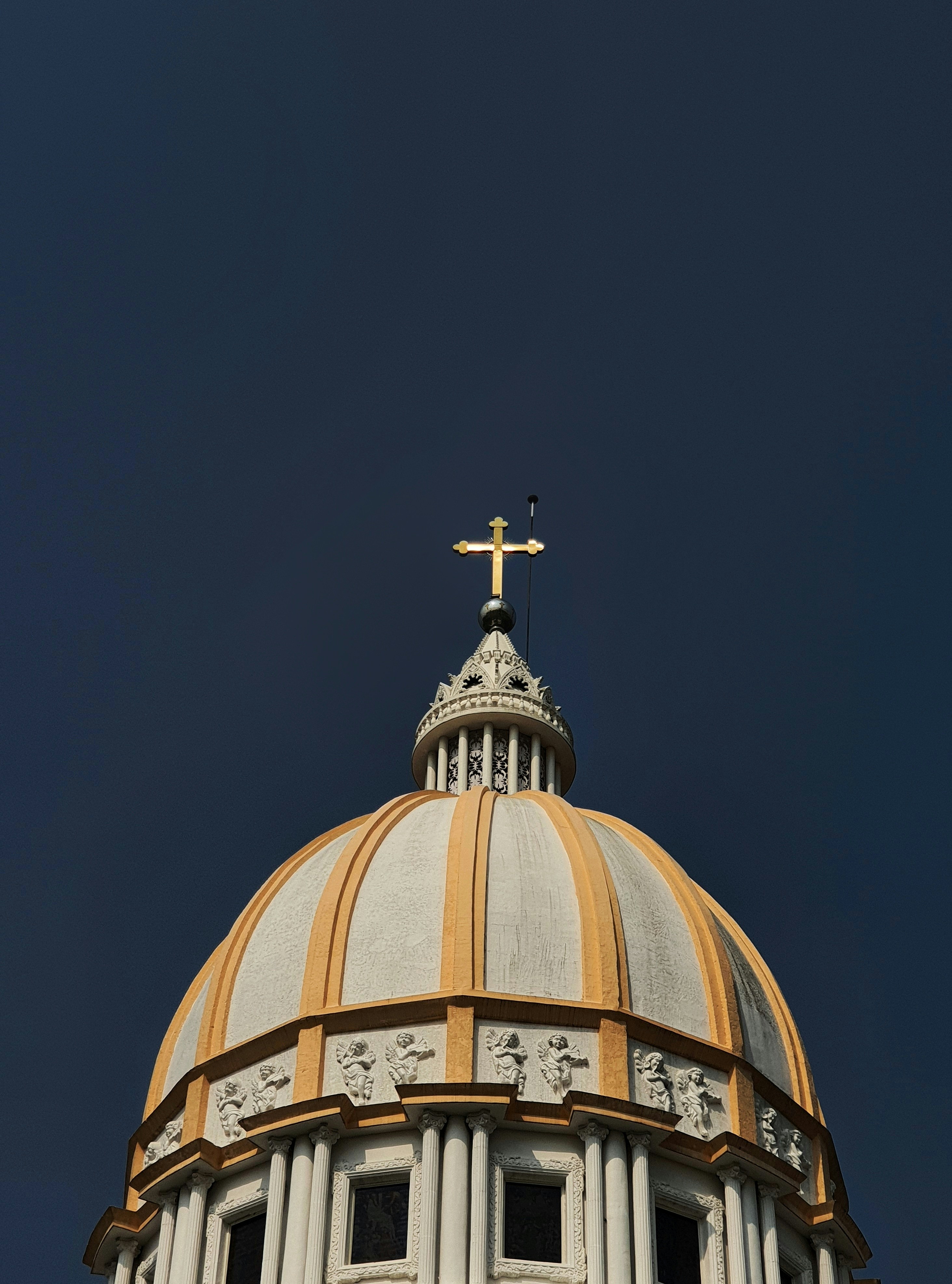 Dome of a historic building topped with a golden cross, set against a dramatic dark sky.