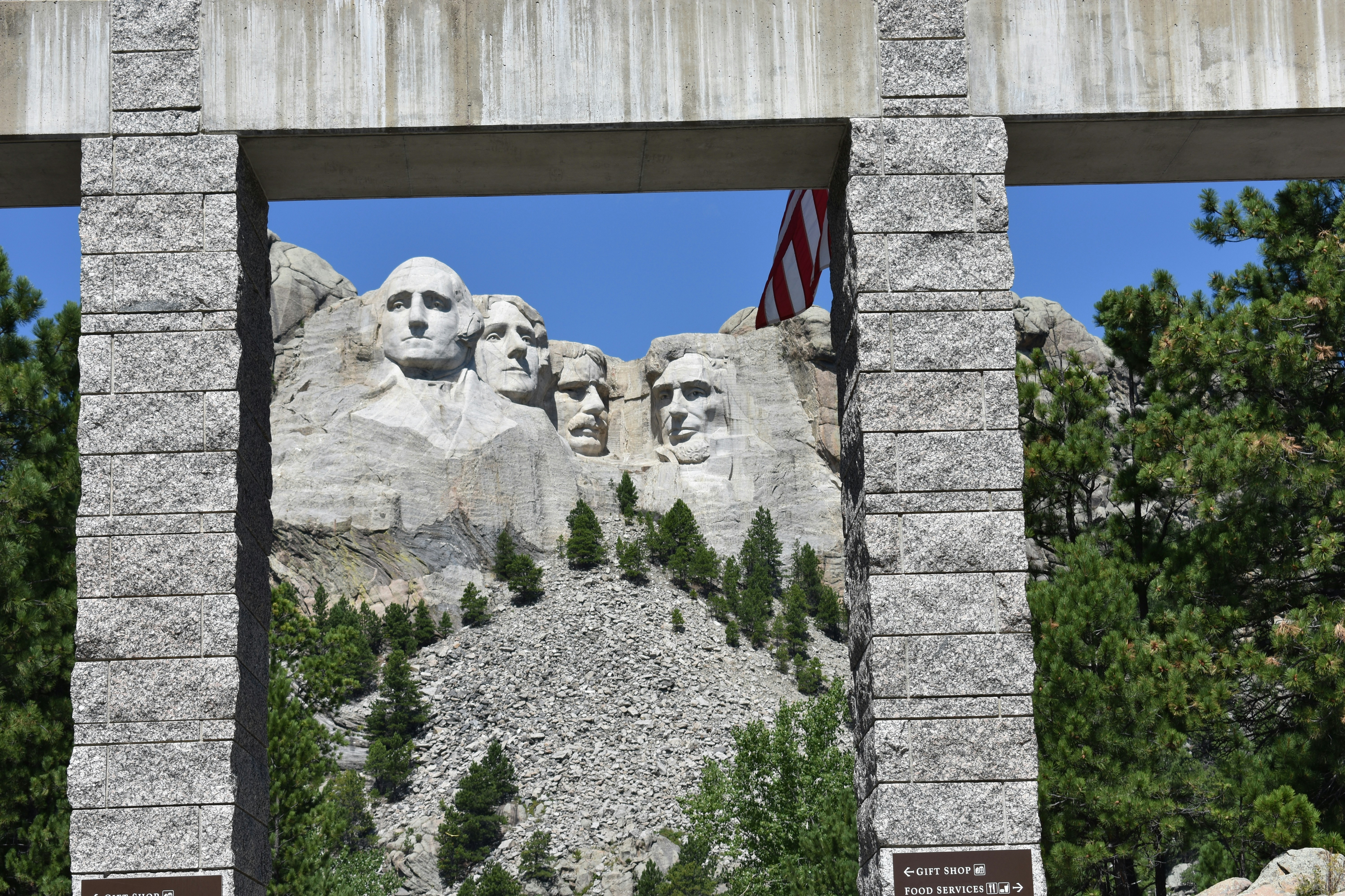 Mount Rushmore's iconic presidential faces framed by stone pillars and a hint of the American flag above. The scene captures the grandeur of this national monument.
