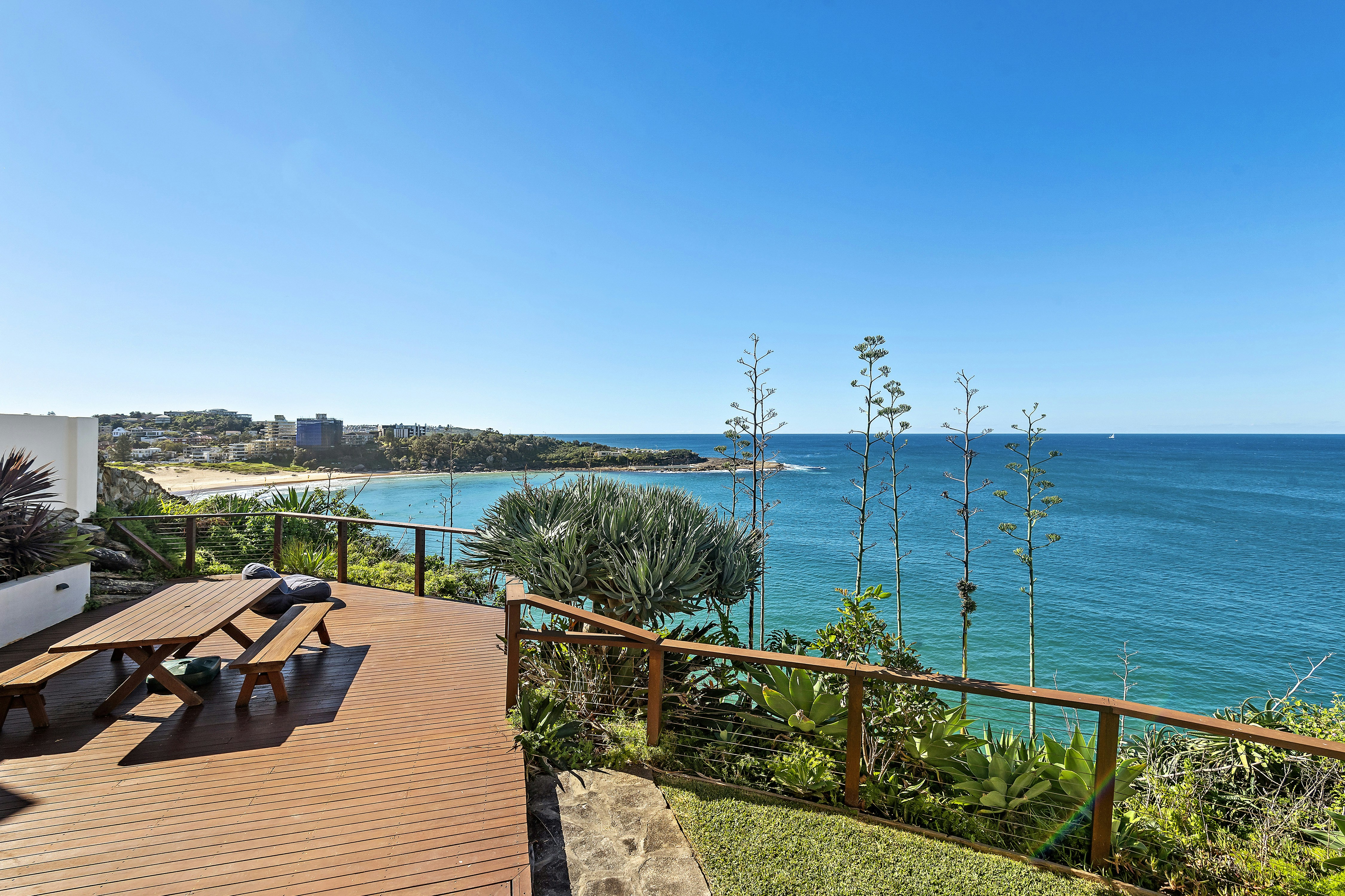 Scenic view from a wooden deck featuring lush greenery and a calm ocean, highlighting a serene coastal landscape.