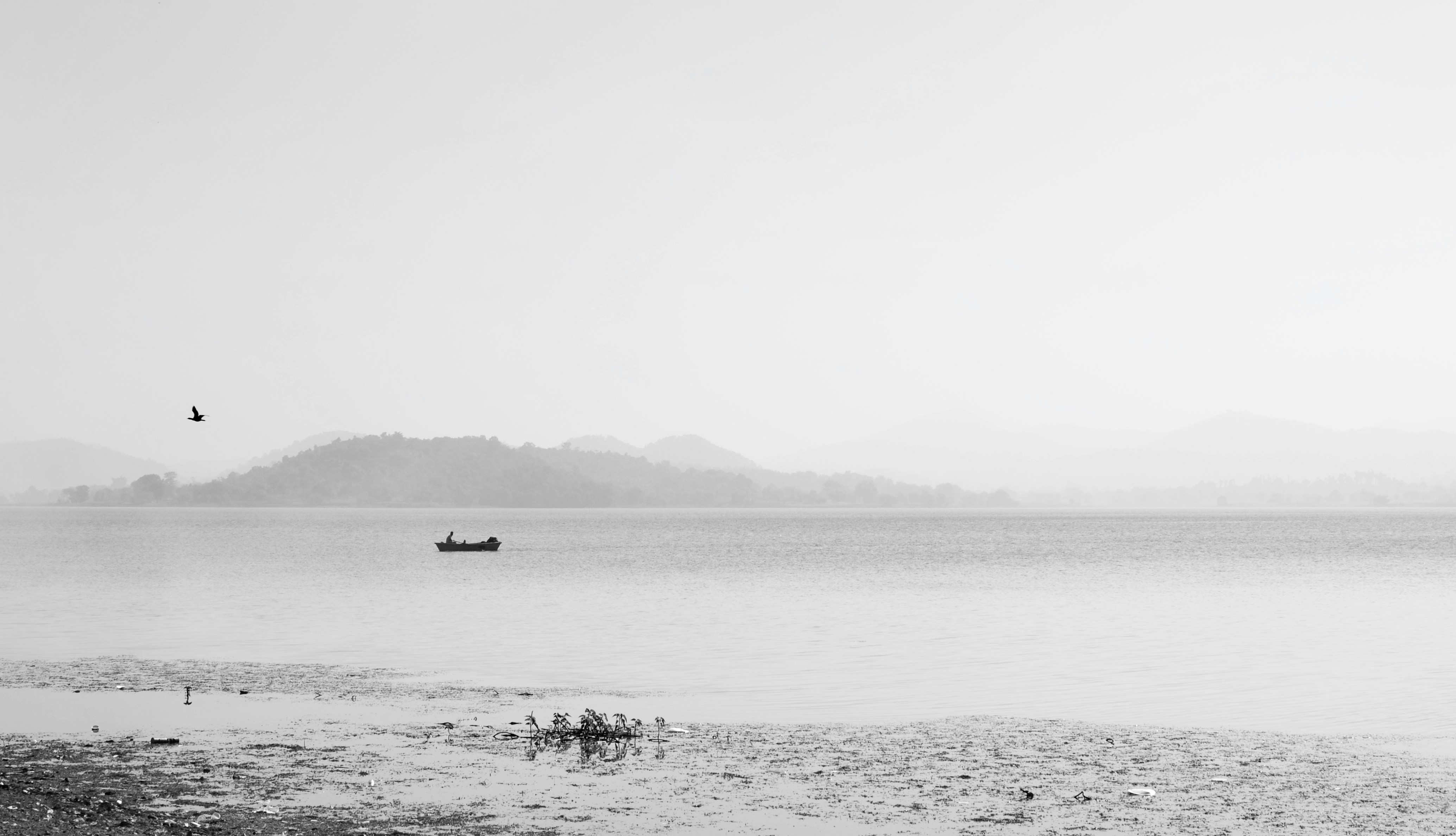 Two individuals in a boat on a calm sea with distant hazy mountains.