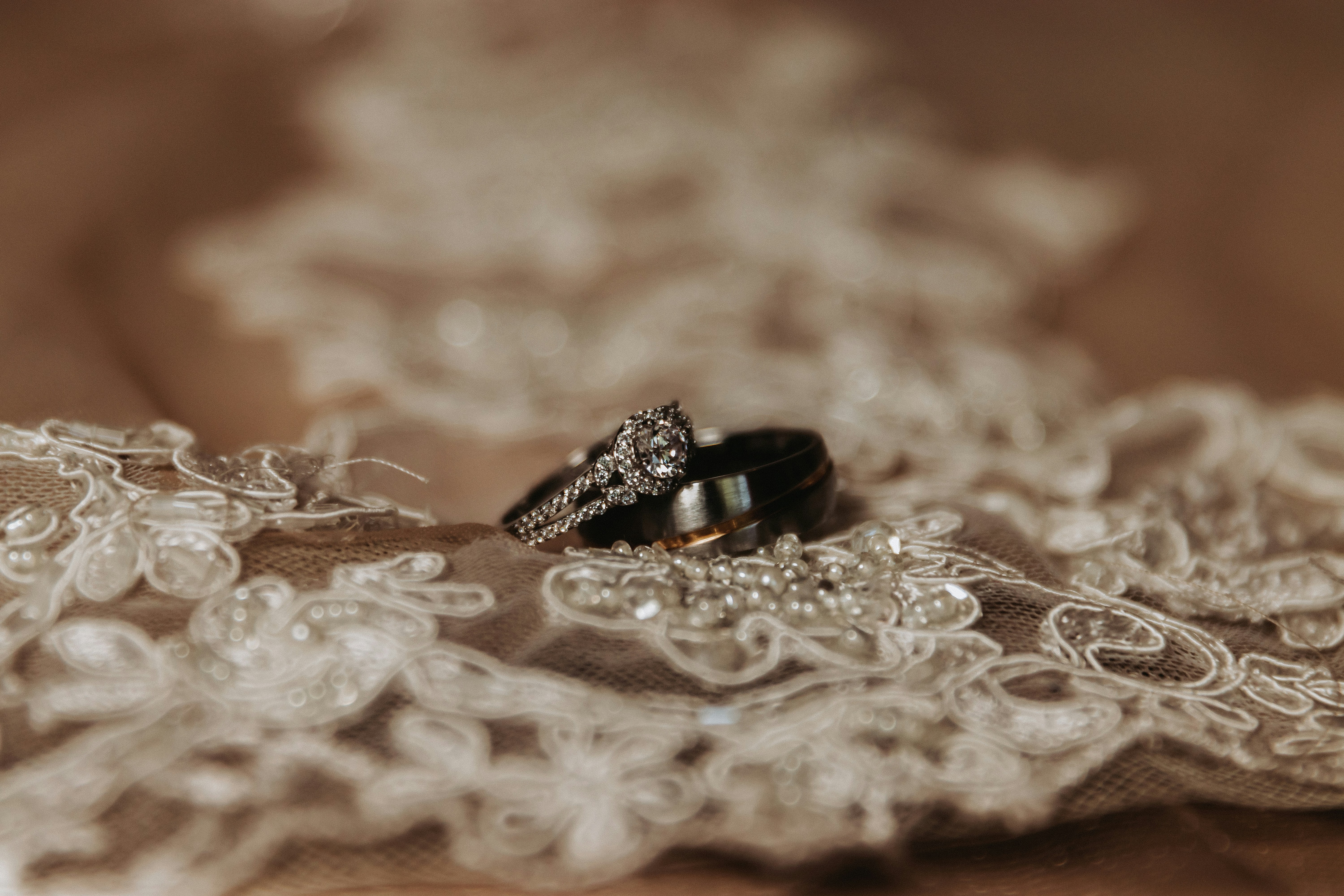 Wedding rings resting on intricate lace fabric with pearls.