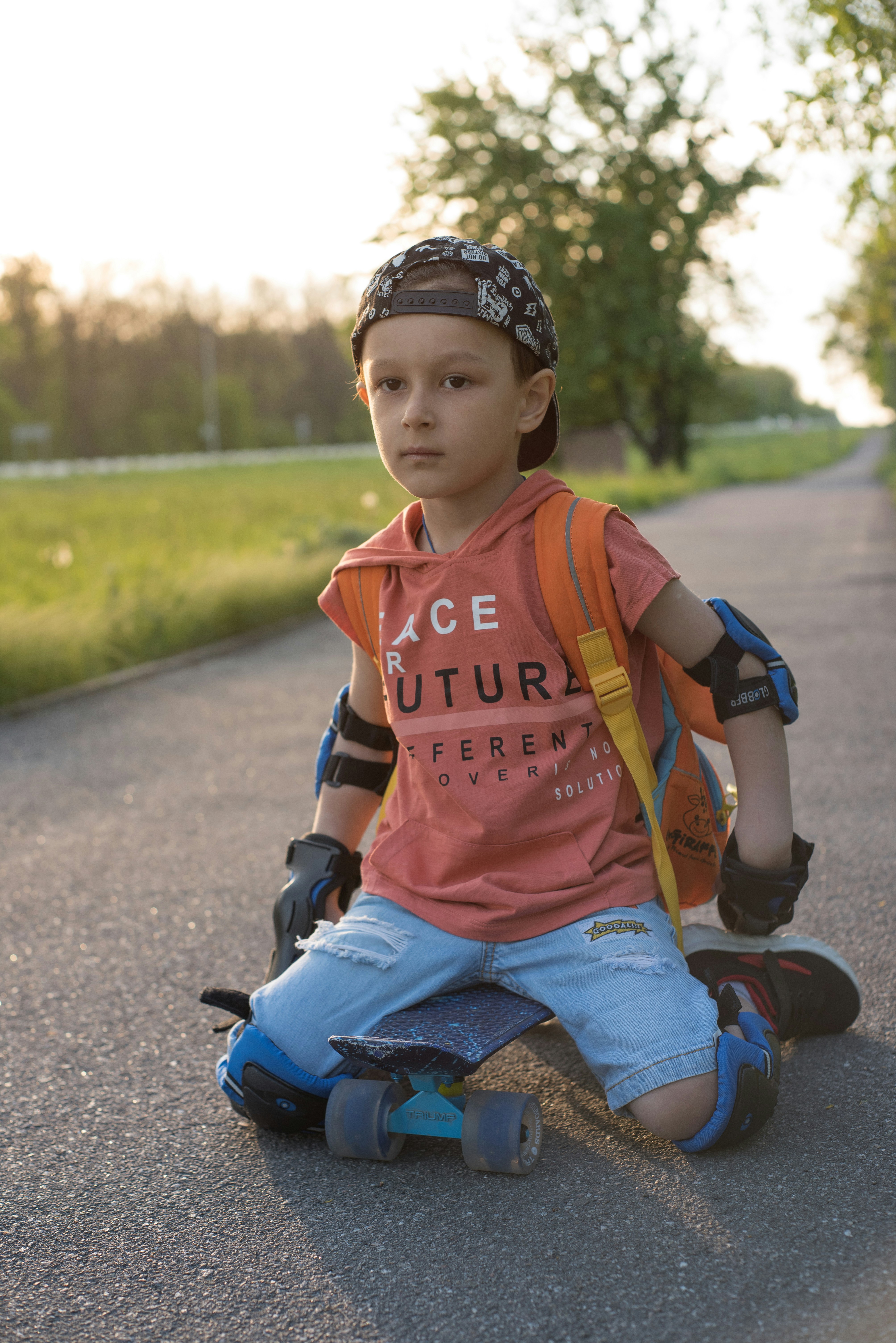 Child wearing protective gear sitting on rollerblades along a sunlit path surrounded by greenery.