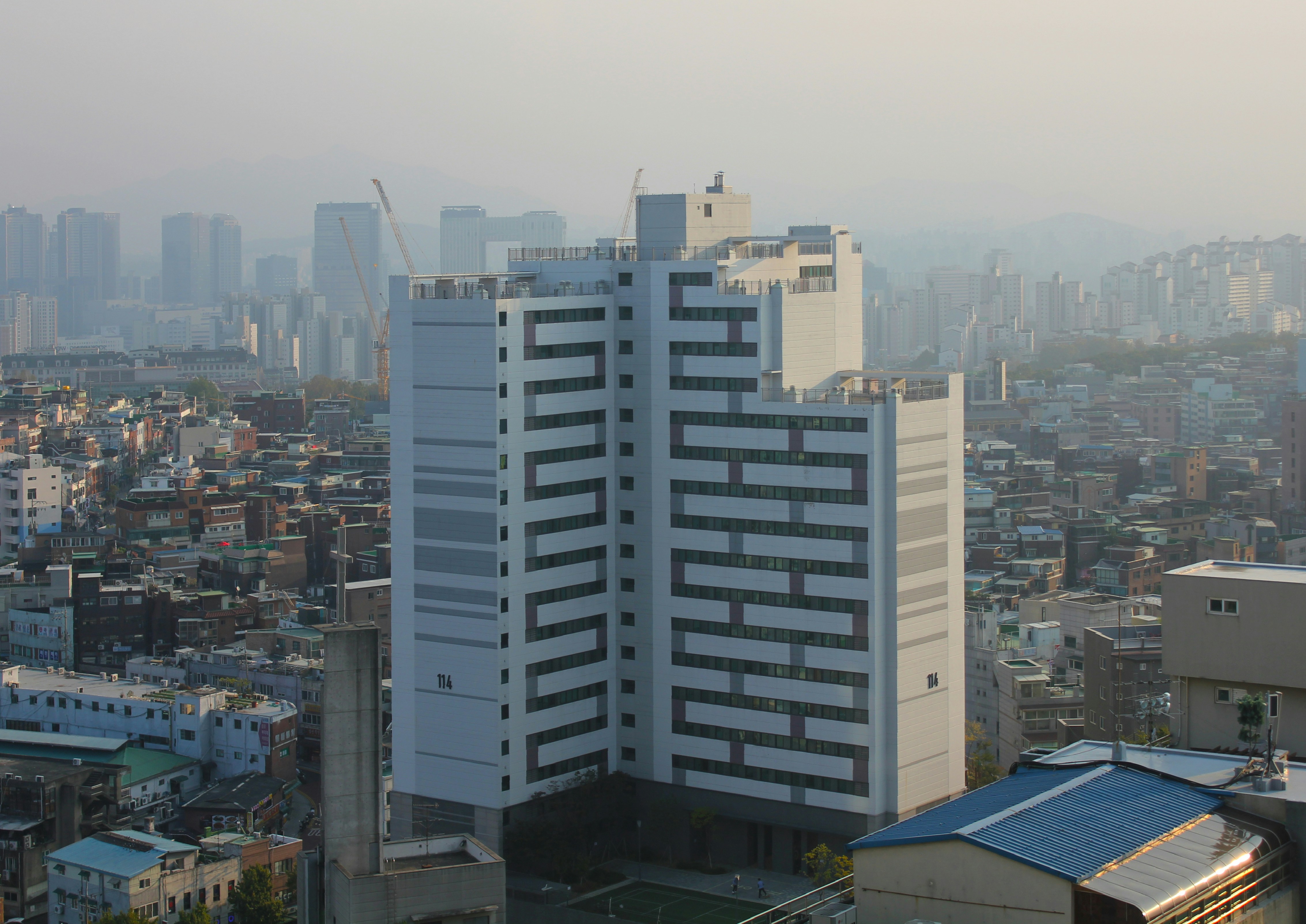 Contemporary building stands prominently against a backdrop of densely packed urban structures, showcasing the contrast between modern architecture and traditional cityscapes.