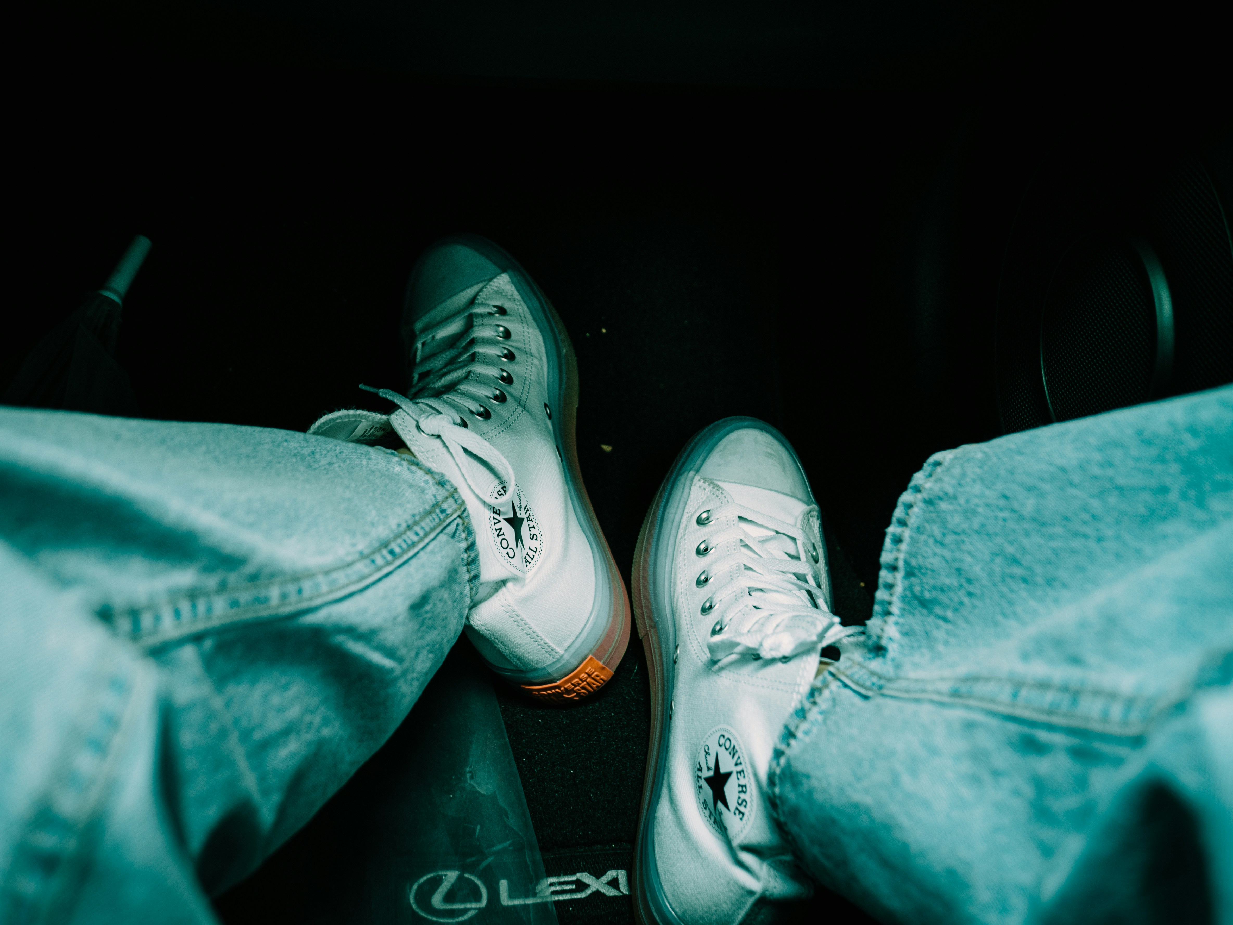 Stylish white sneakers resting on a car floor mat, surrounded by casual denim attire. The scene captures a moment of urban exploration.