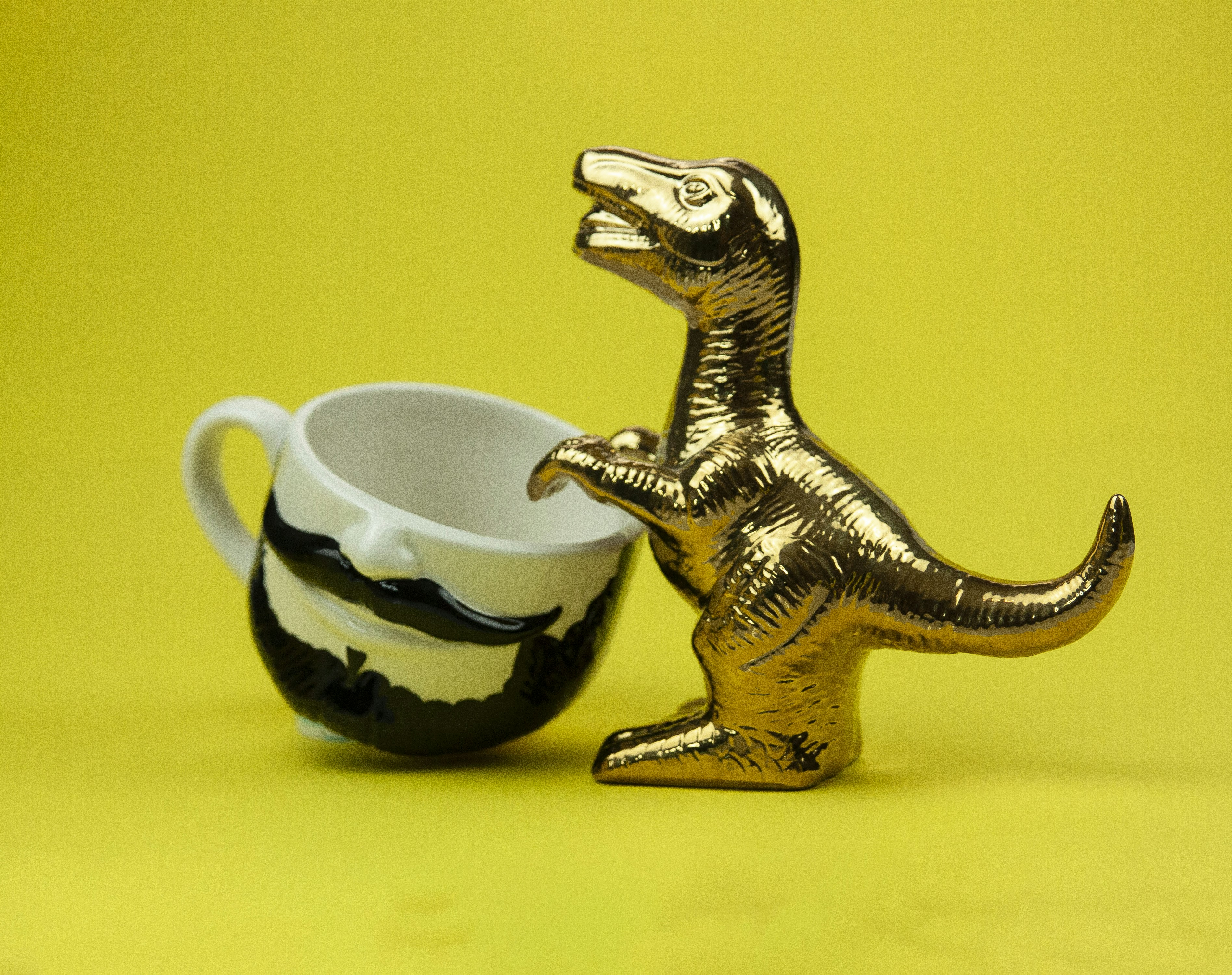 Gilded Dinosaur Guarding a Ceramic Cup on a Canary Yellow Stage