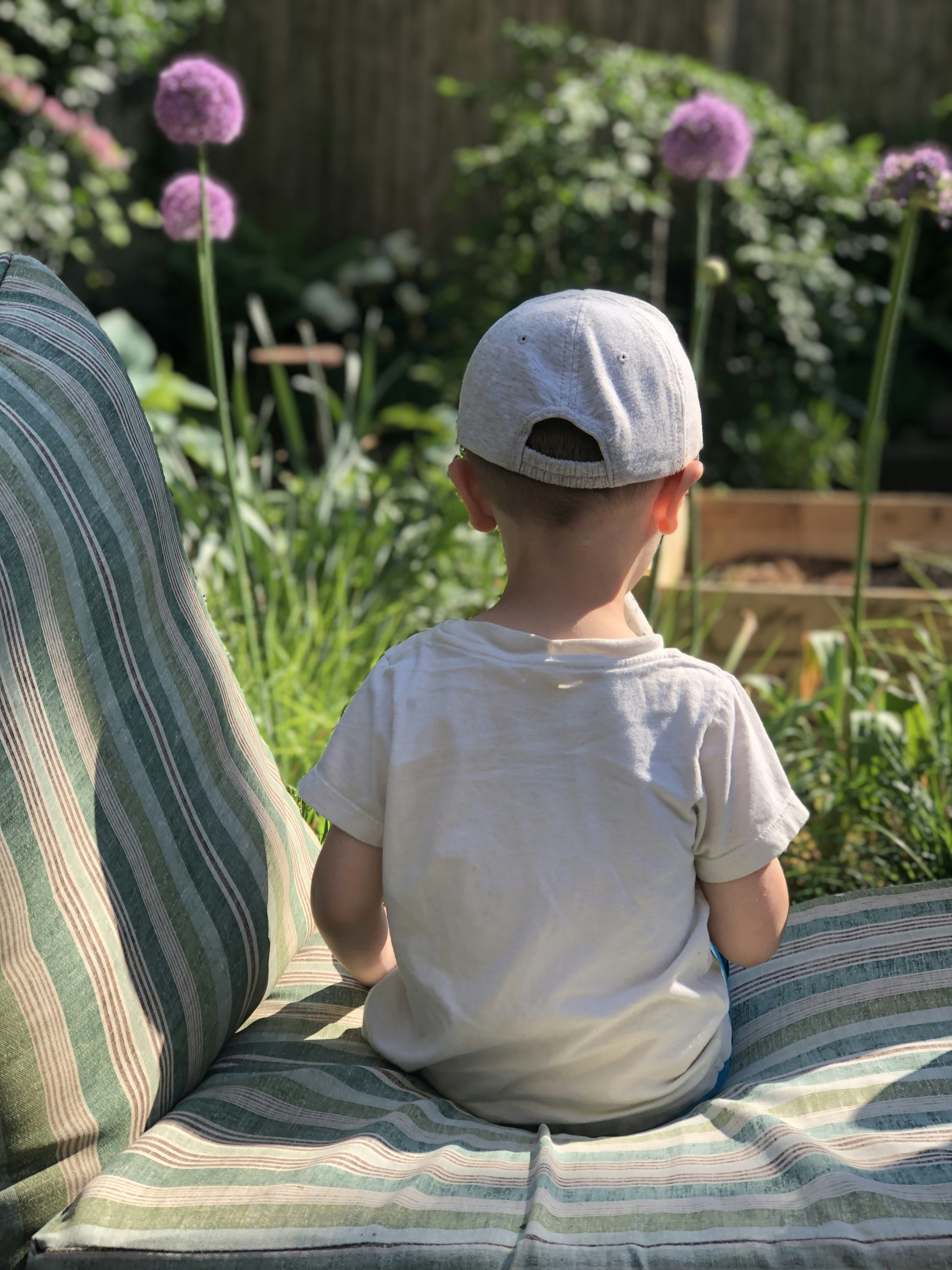 Child on a striped bench facing a flower garden