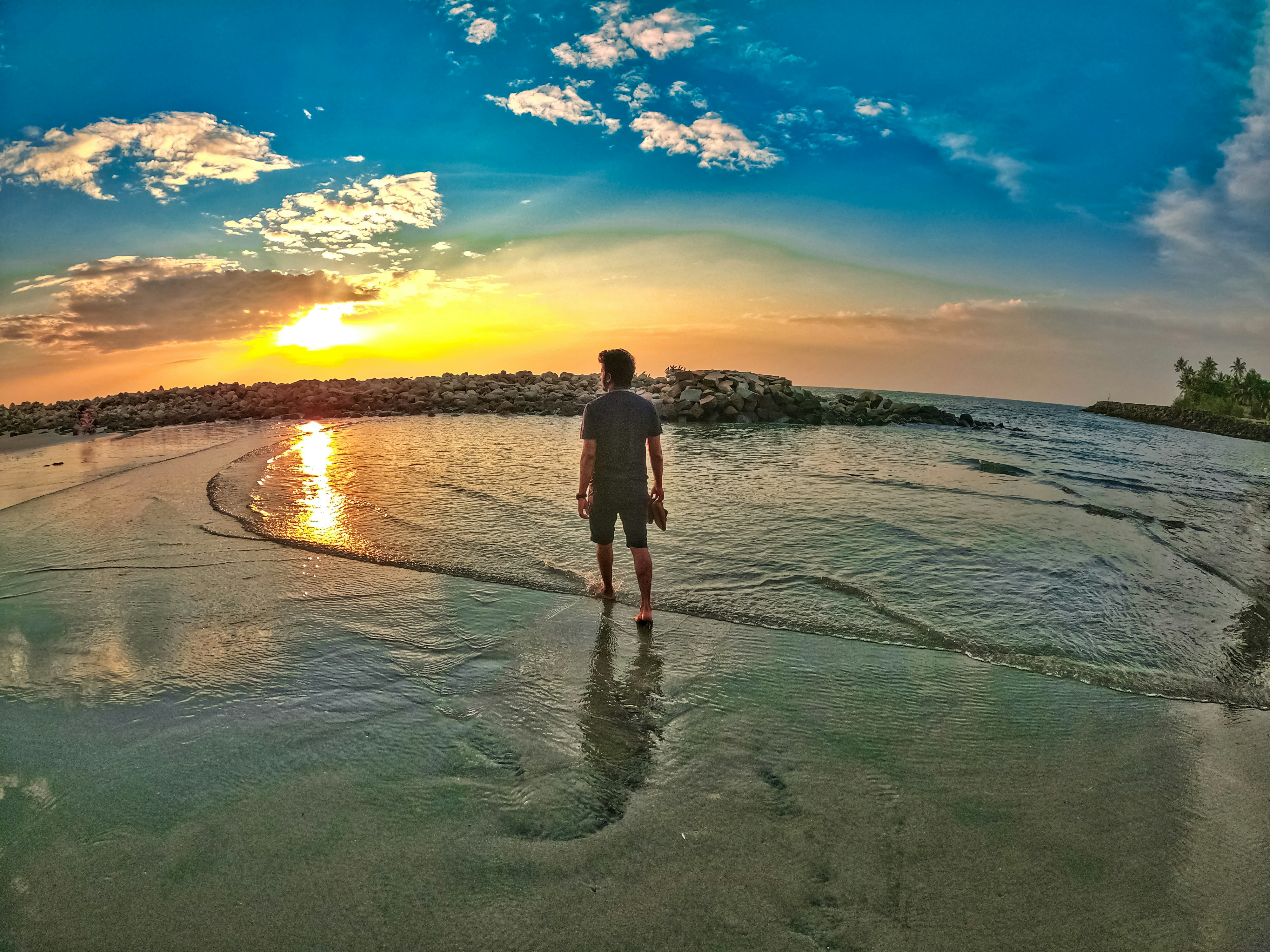 Silhouetted figures walk along a serene beach at sunset, with vibrant sky reflections on the wet sand.