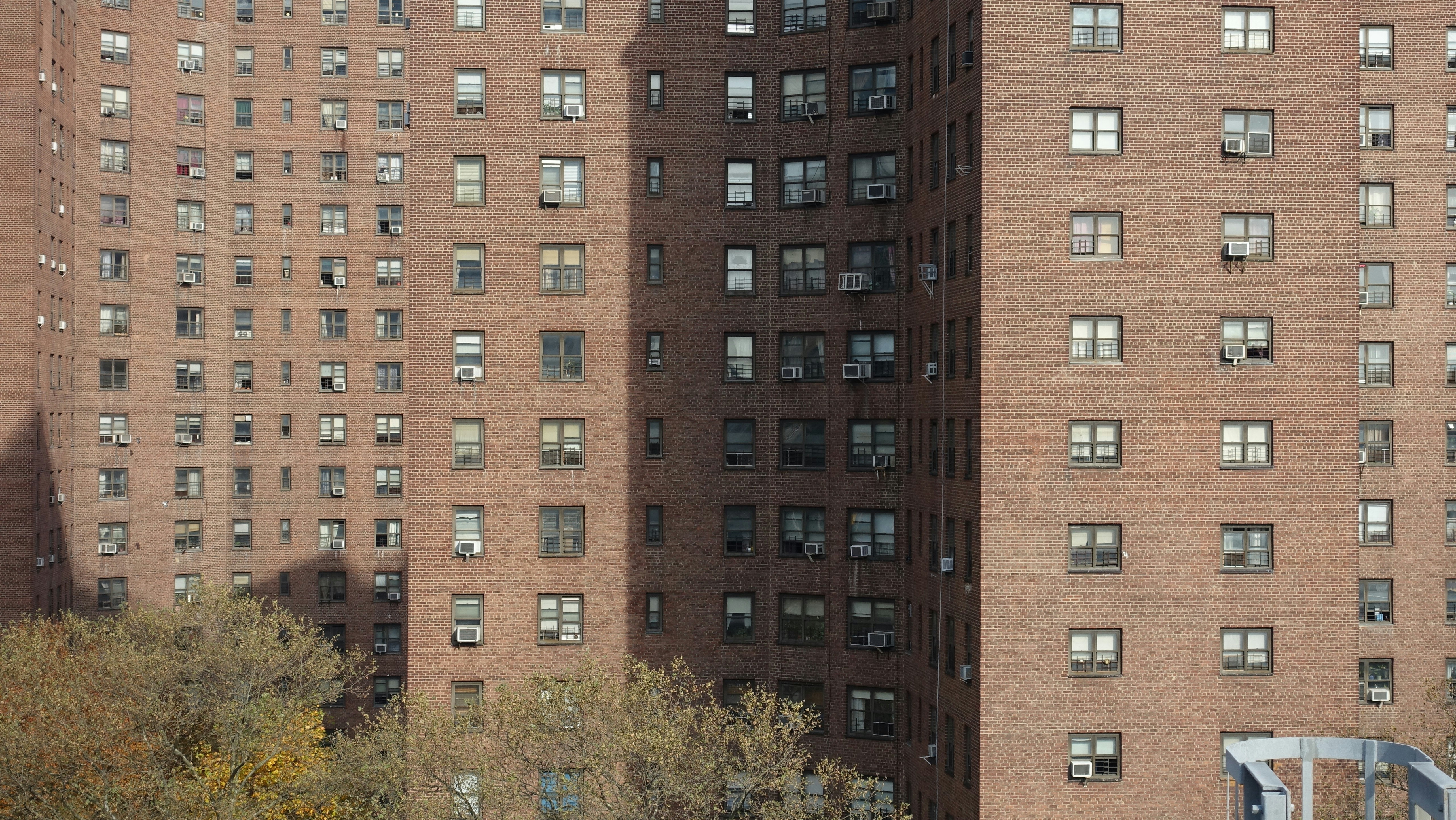 Red brick apartment buildings with numerous windows, showcasing urban architecture and life. The scene captures the interplay of light and shadow across the structure.