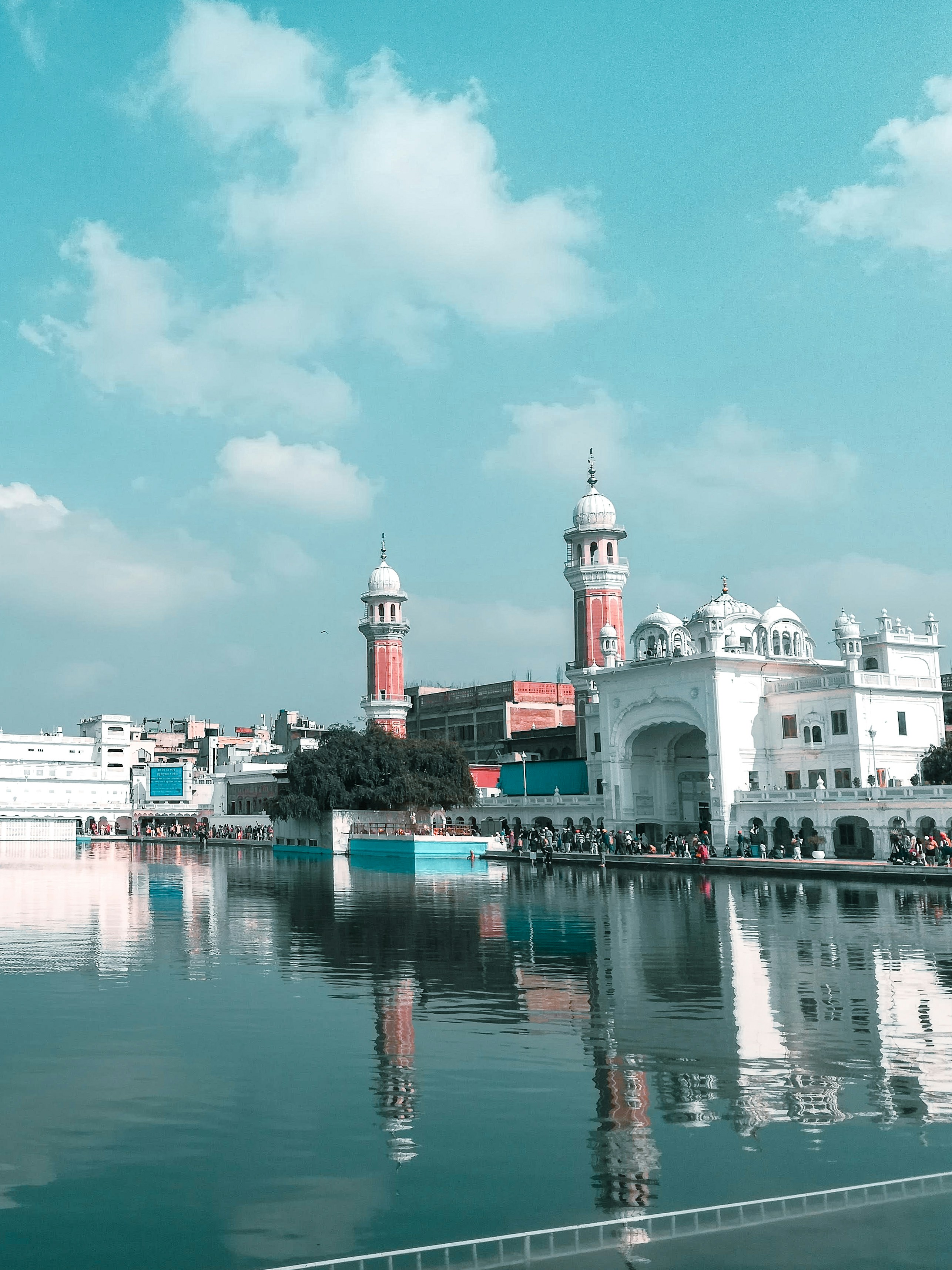 Majestic white structure with intricate architecture reflected in tranquil water, surrounded by vibrant buildings and a clear blue sky.
