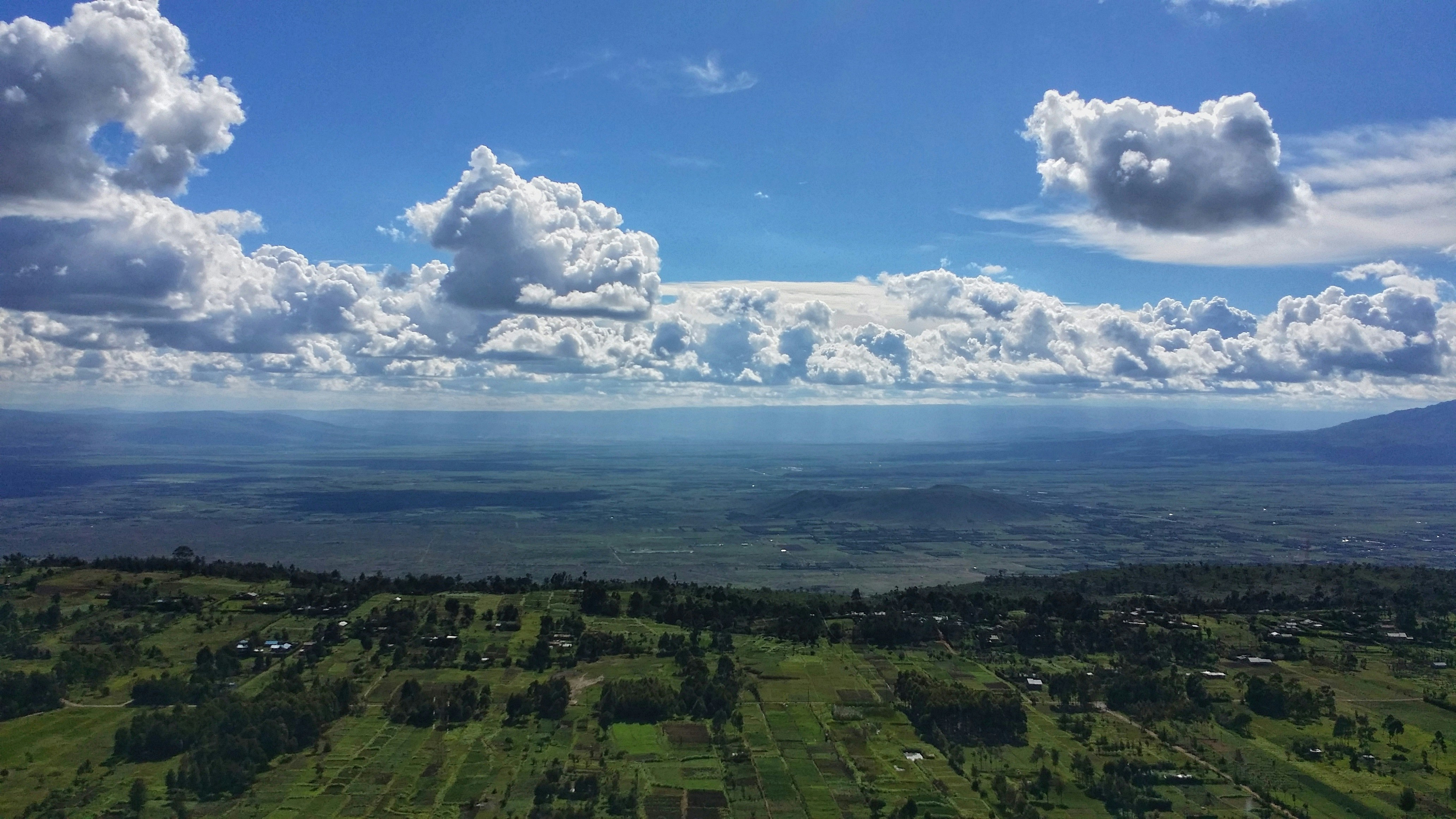 Rolling green landscape beneath a sky filled with billowing clouds and bright sunlight.