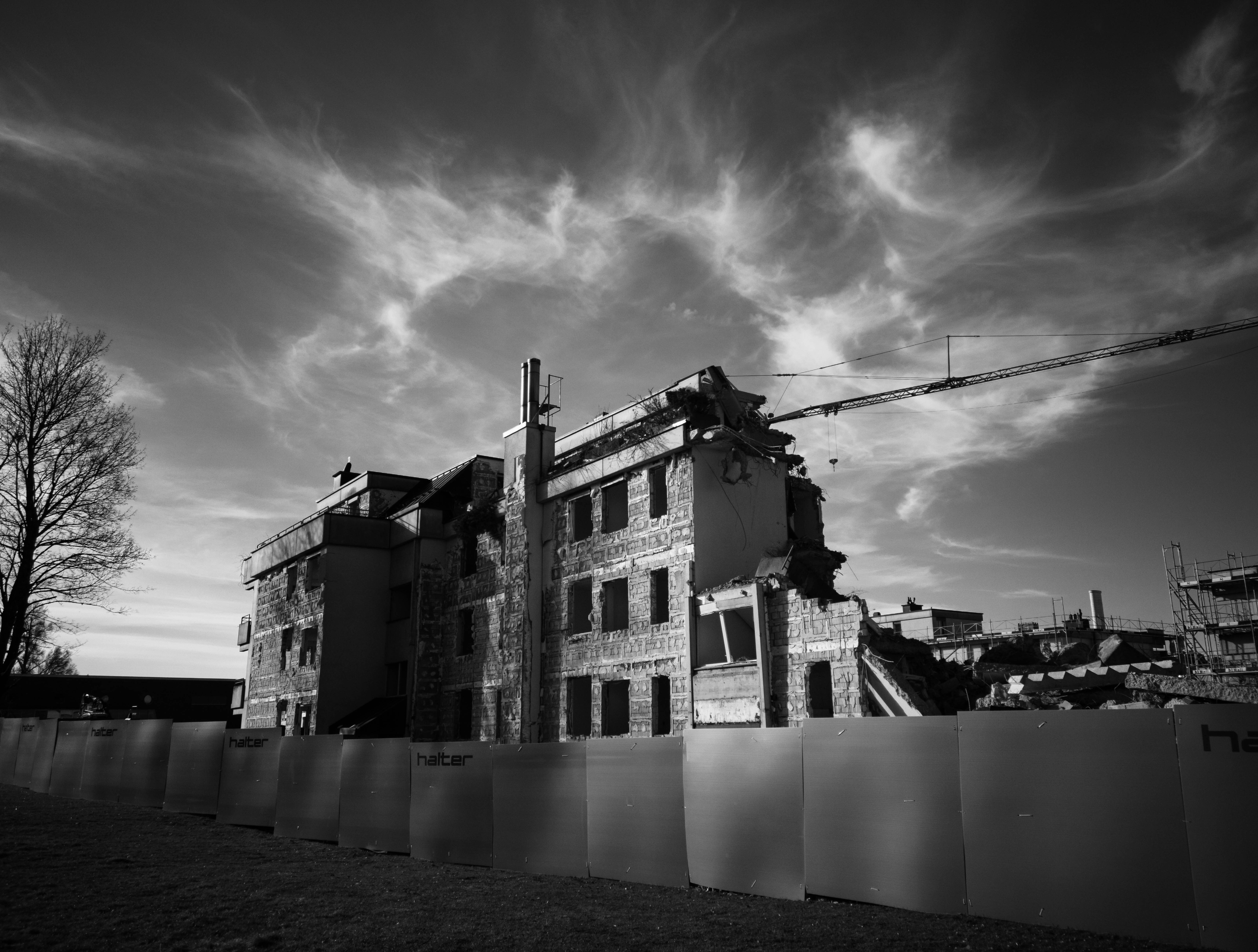 Dilapidated building stands against a dramatic sky, surrounded by construction barriers. The scene captures the essence of urban decay and transformation.