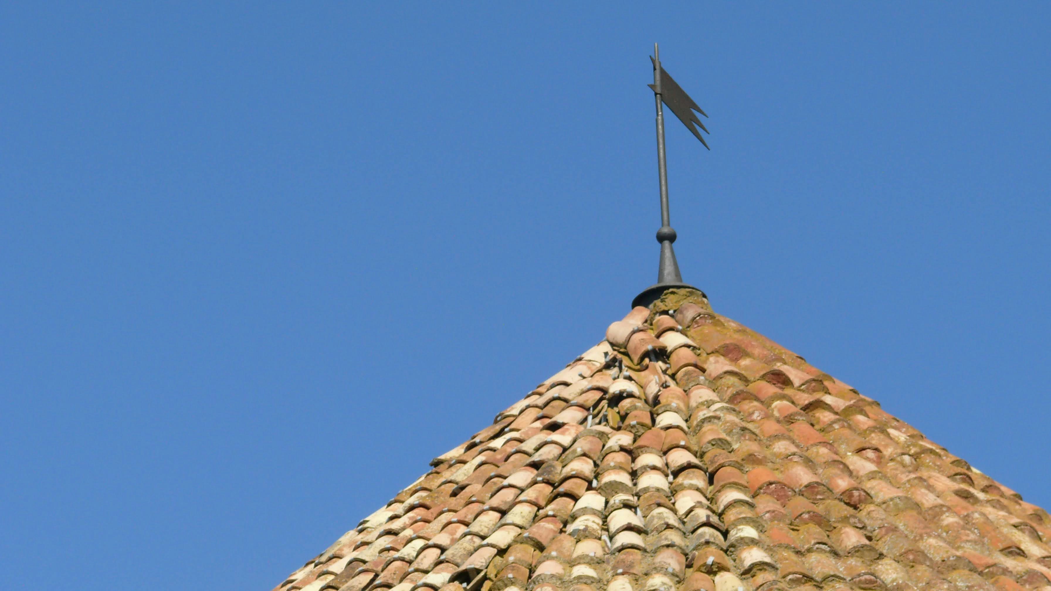 Apex of Clay-Tile Roof under a Weather Vane against a Clear Azure Sky