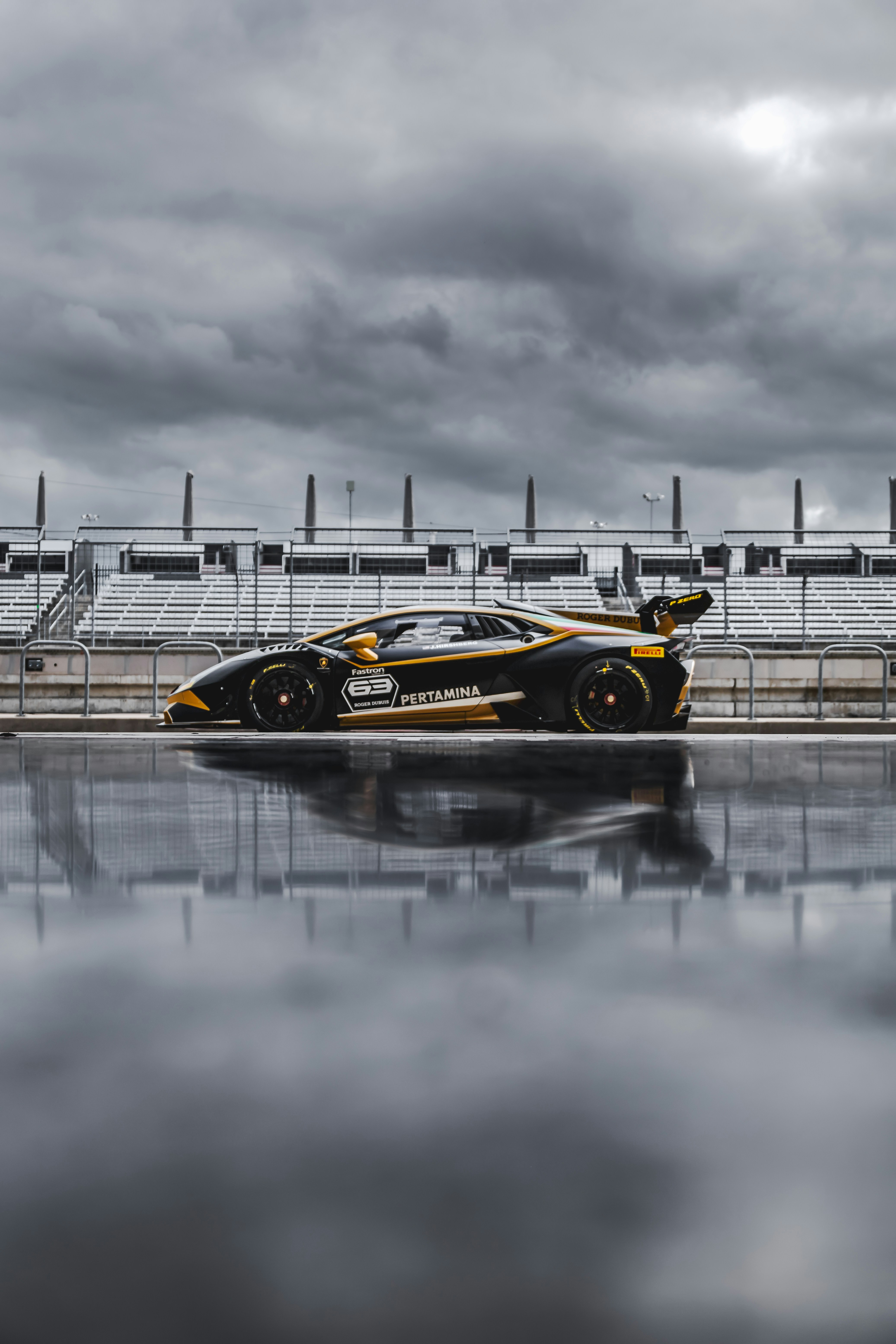 A sleek racing car parked on a reflective surface under a moody sky, showcasing its aerodynamic design and vibrant branding.