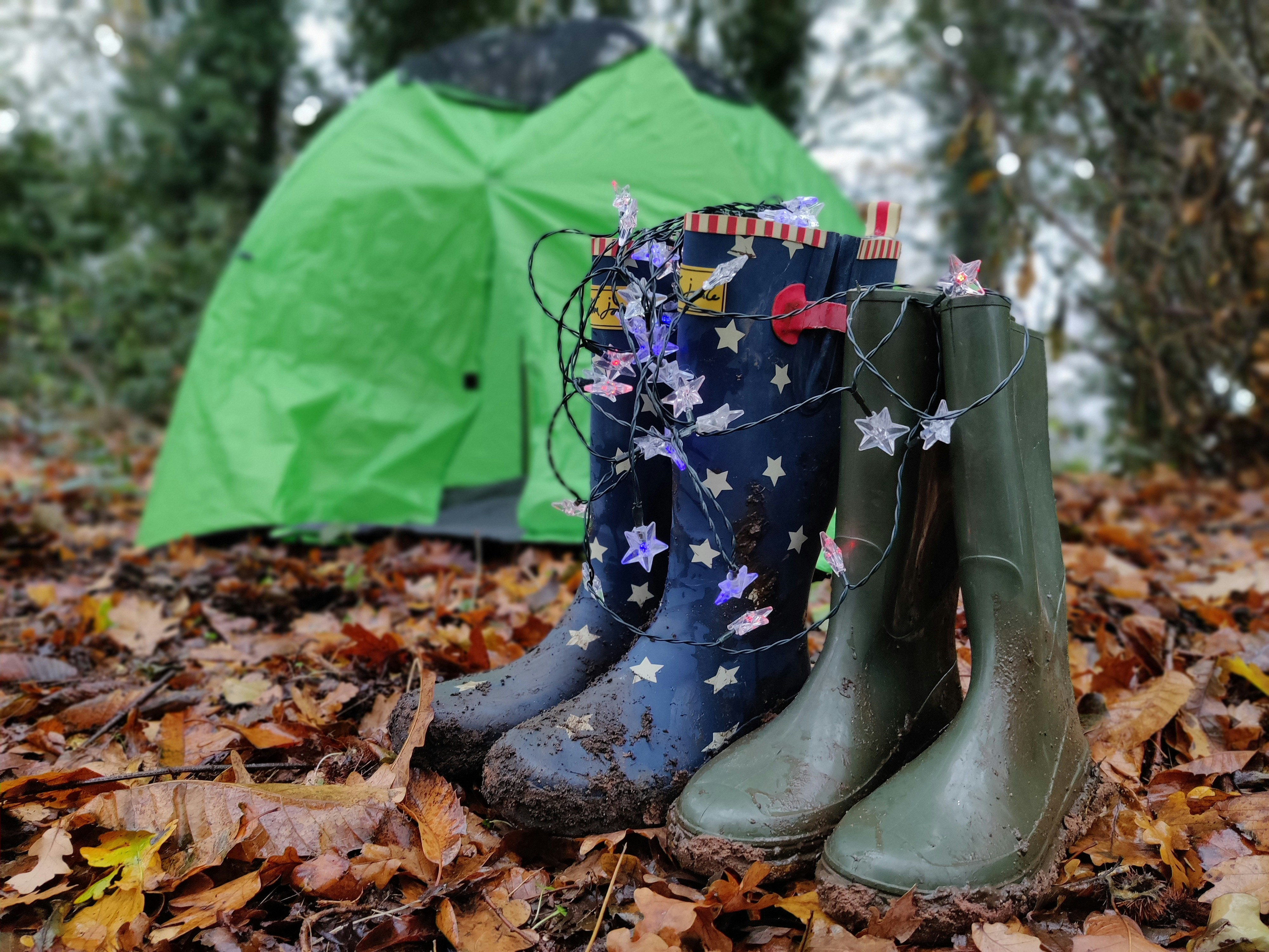Decorated boots with fairy lights on leaf-strewn ground next to a bright green tent.