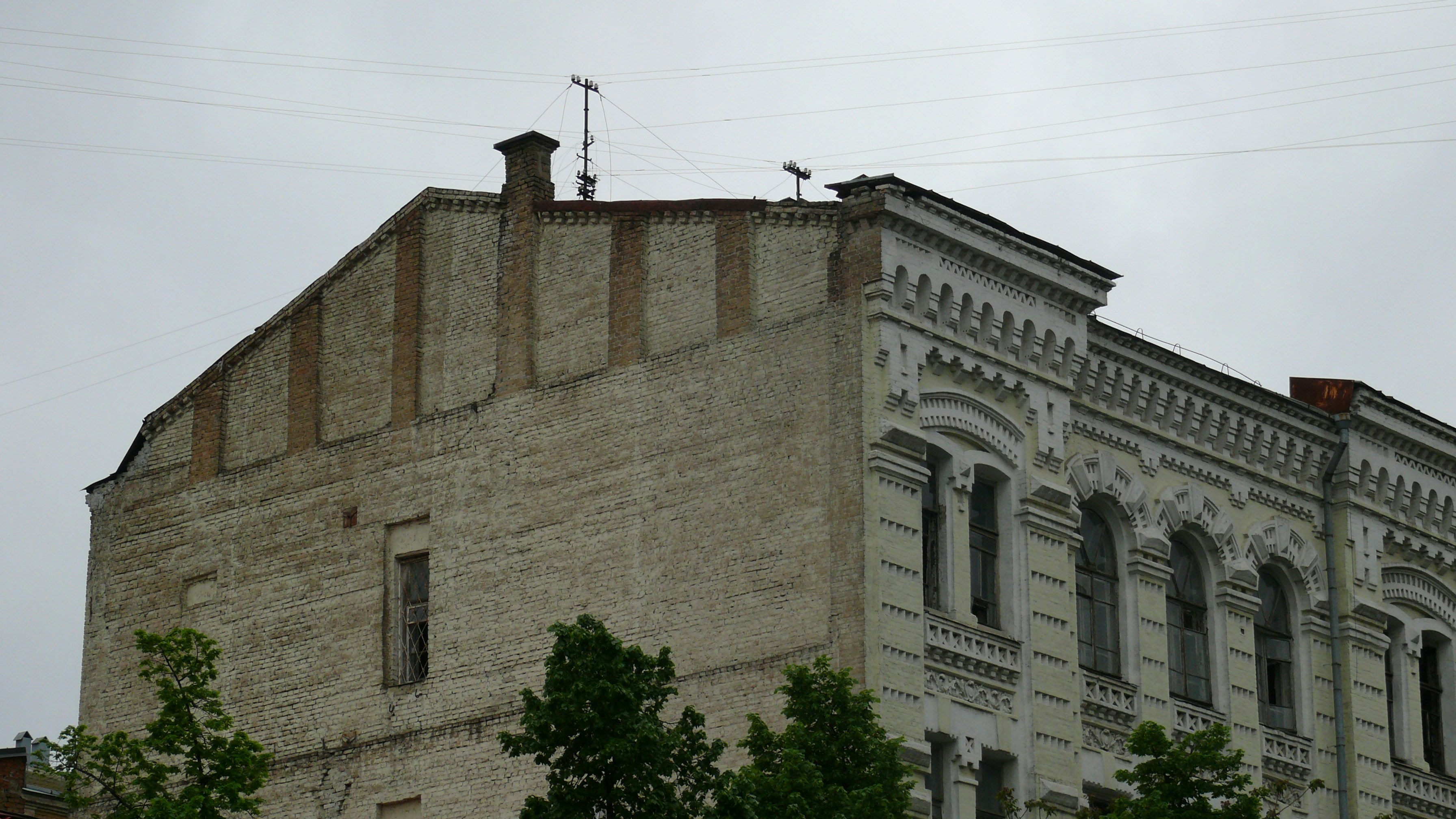 Historic building featuring intricate architectural details and a weathered facade, surrounded by greenery under a cloudy sky.