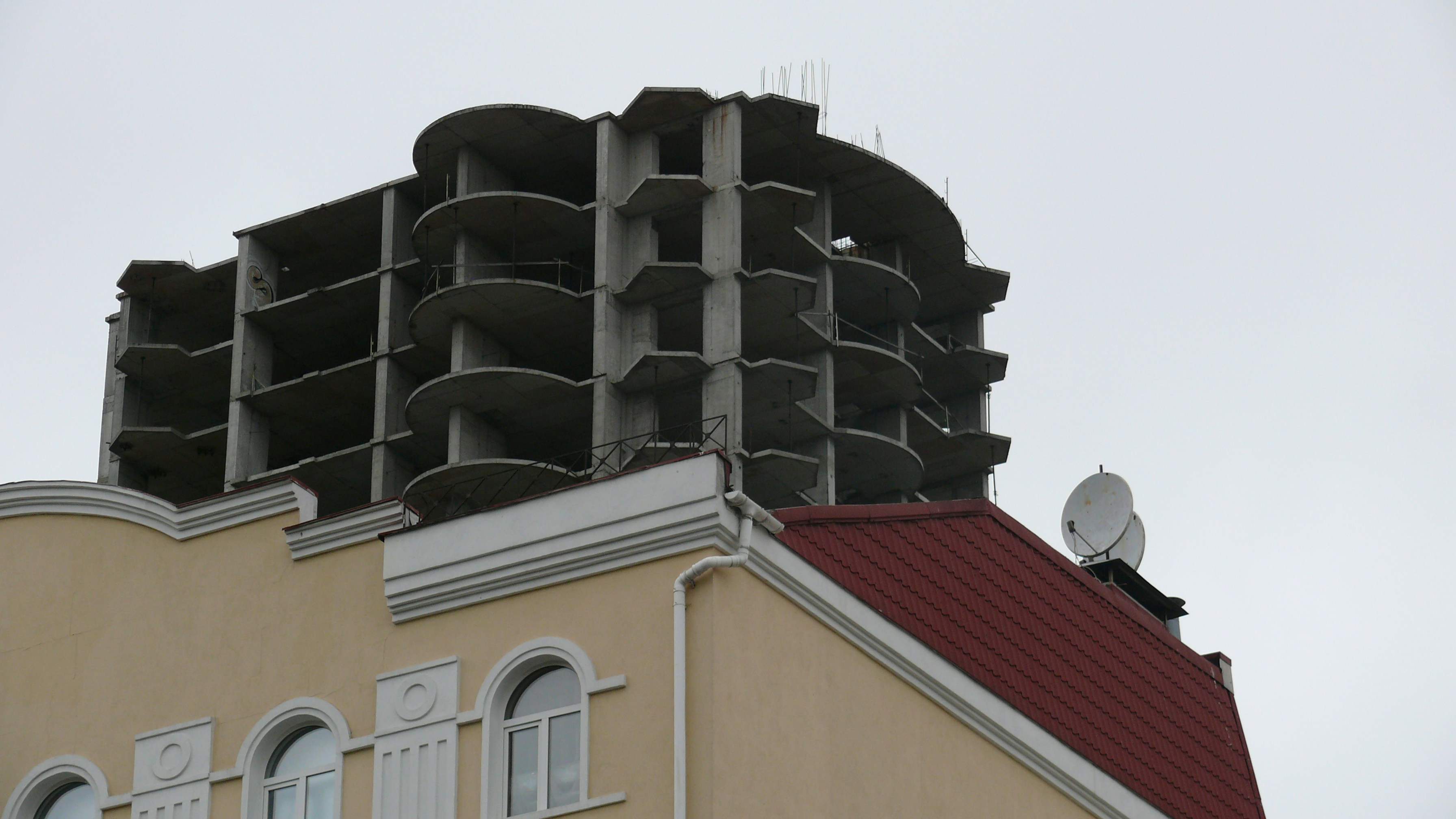 Rooftop Skeleton: Unfinished Concrete Tower Surges Over a Mediterranean-Style Facade