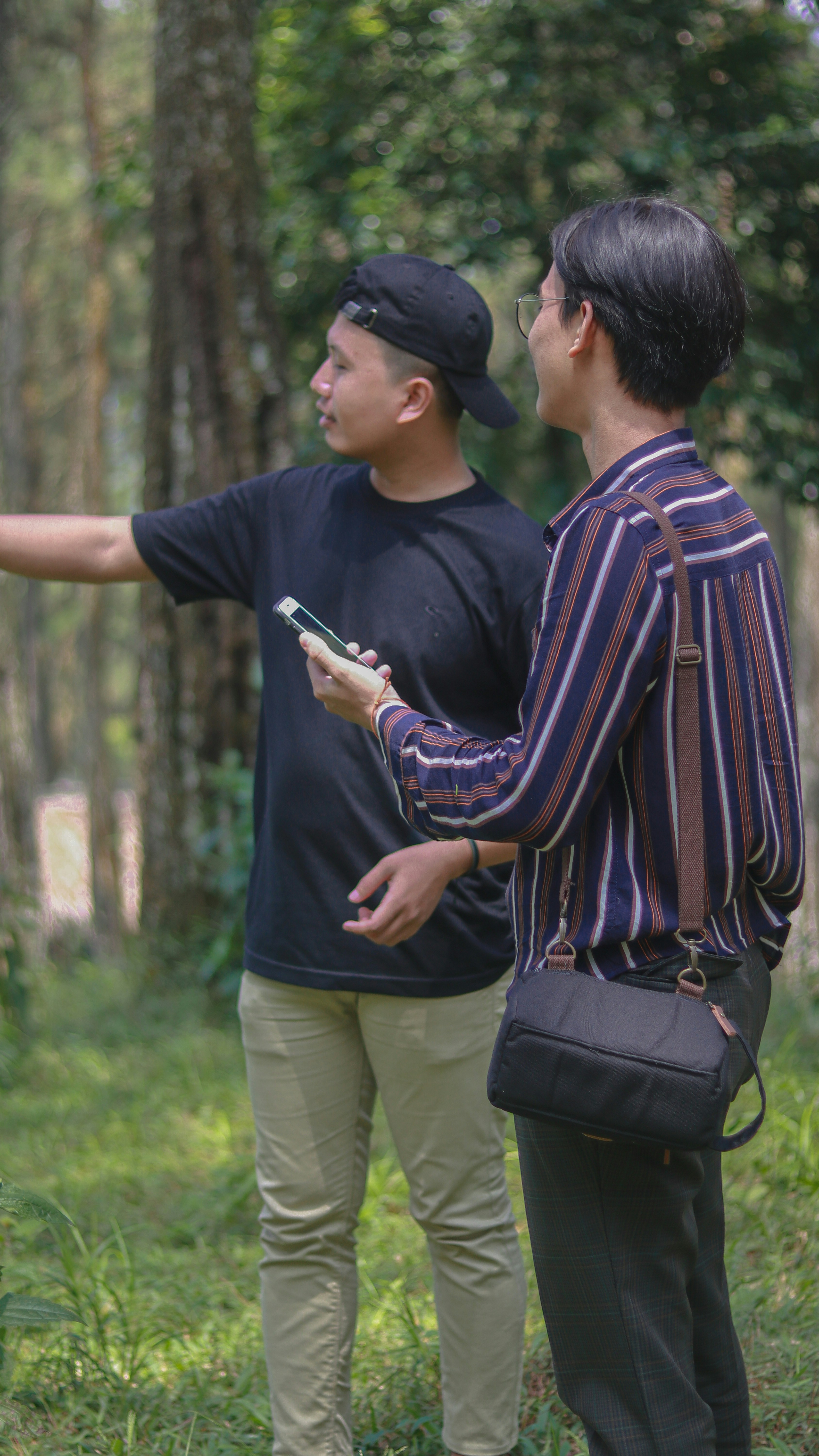 Two individuals engaged in conversation while exploring a lush, green forest, one gesturing towards a point of interest. The scene captures a moment of discovery and connection with nature.