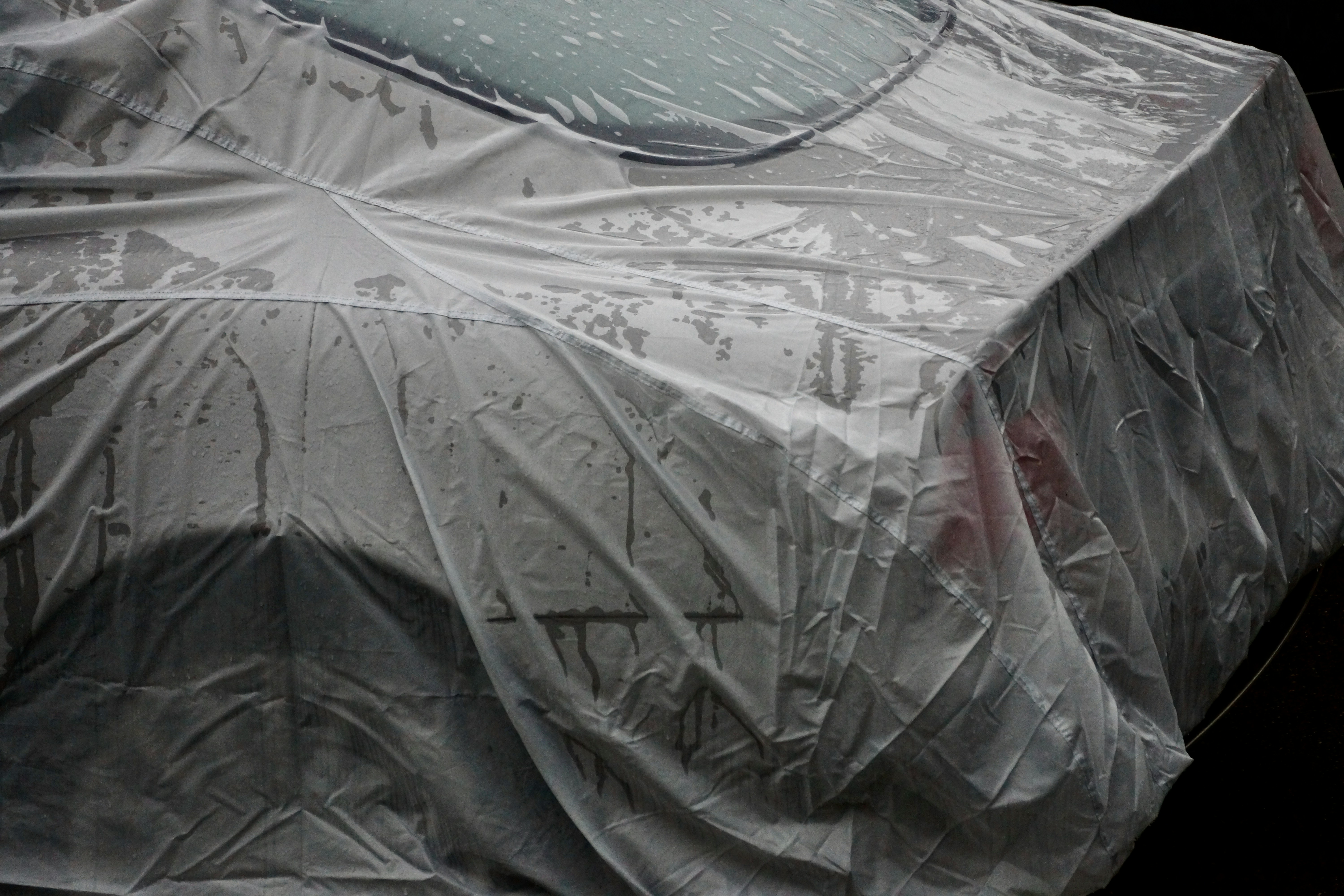 Car covered in a rain sheet on a wet day