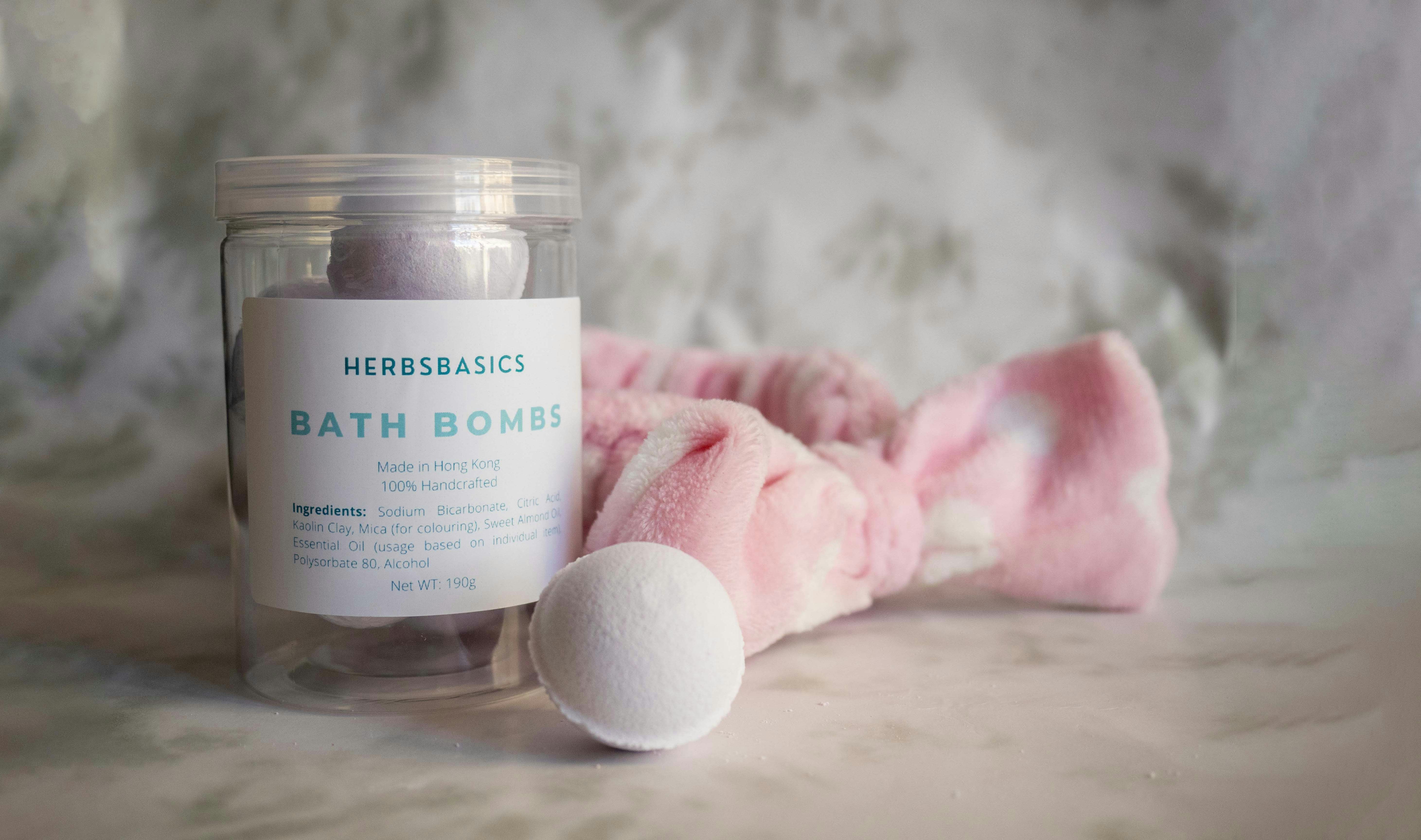 HerbsBasics bath bombs in a clear jar with a pink towel backdrop.