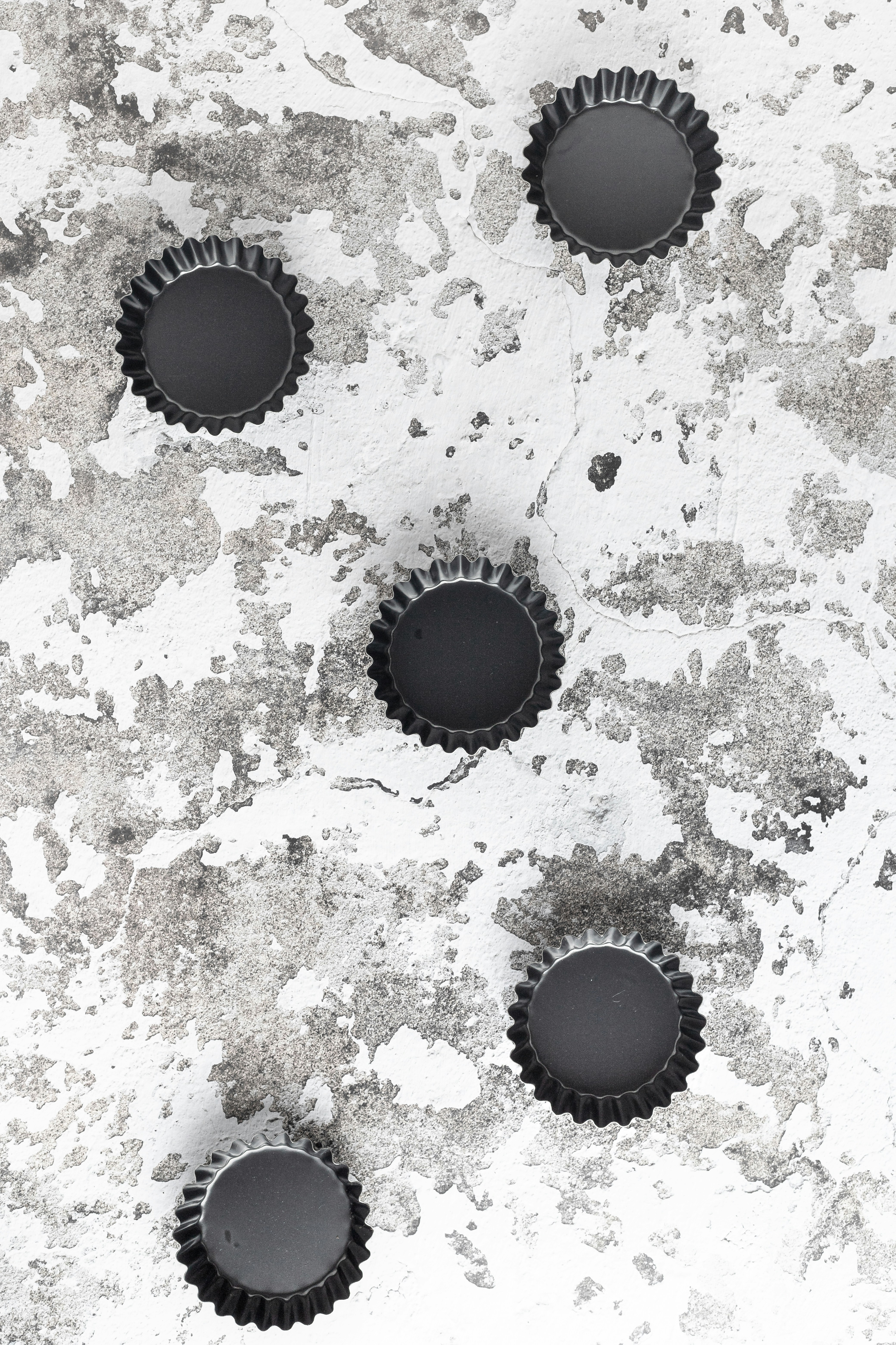 Five Dark Bottle Caps Scatter Across Weathered Concrete
