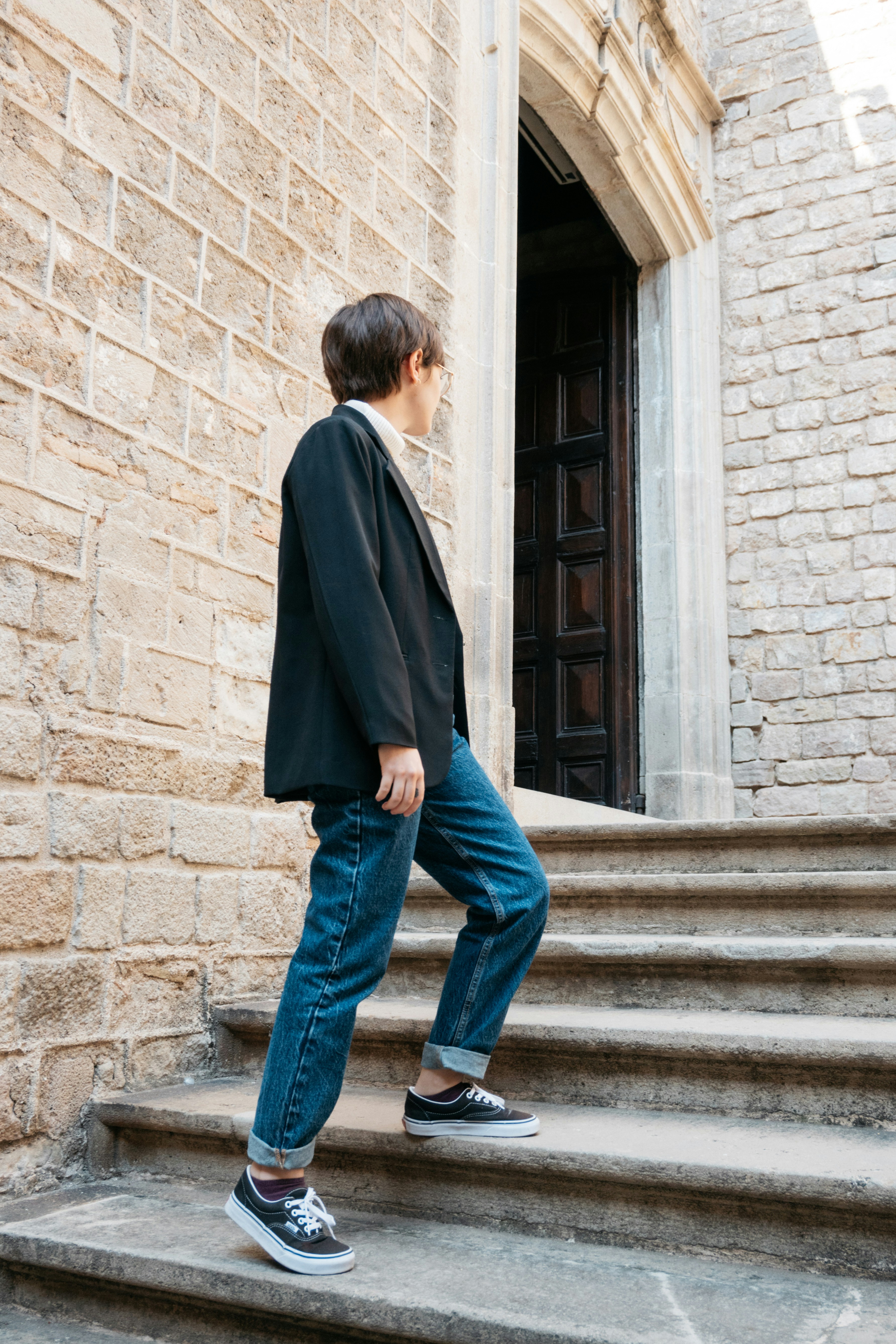 Blazer-Clad Ascent: A Youth Climbing Weathered Stone Steps Toward a Dark Doorway