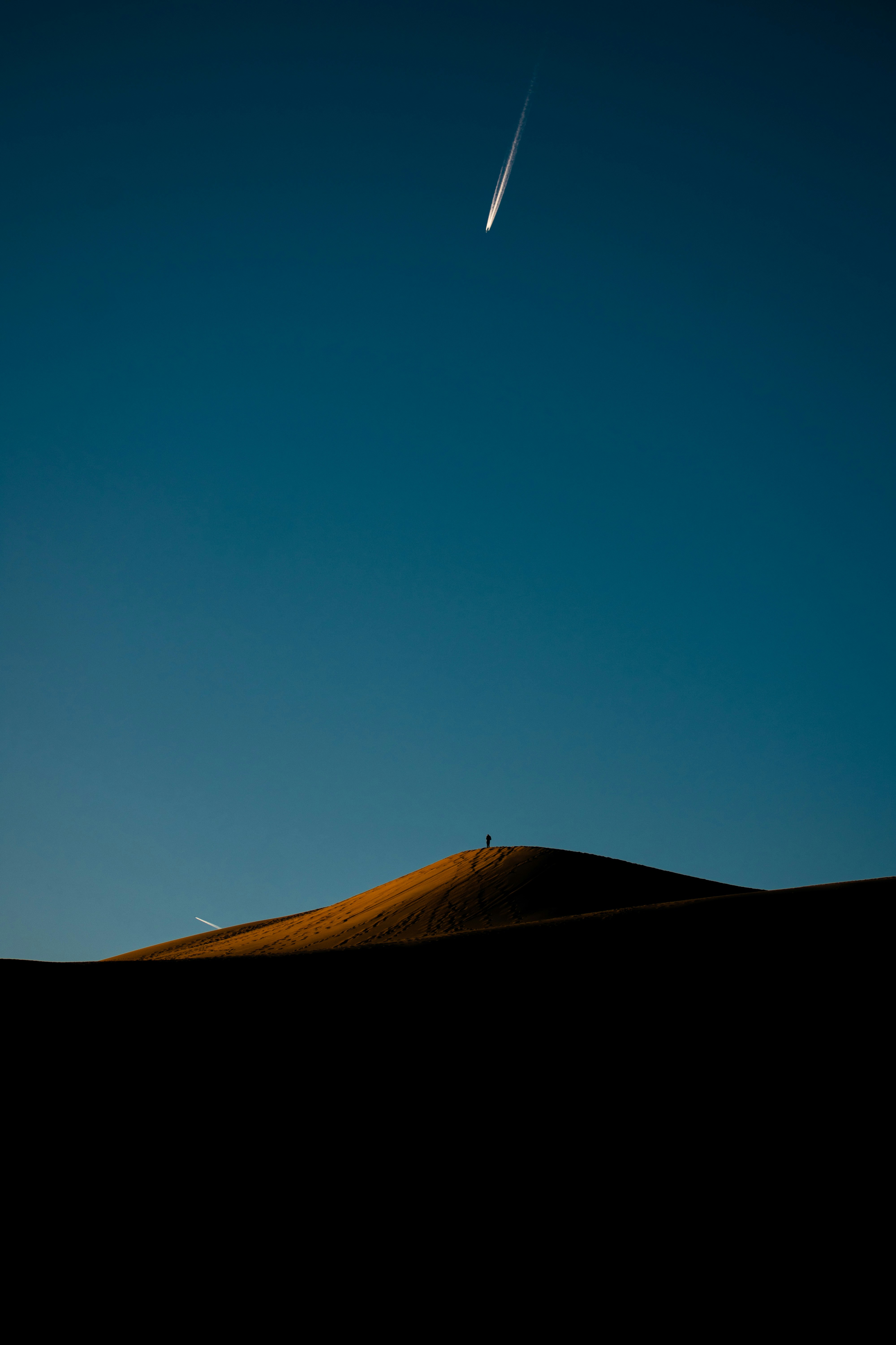 Dune Crest at Dusk: A Lone Figure Beneath a Sky Trail