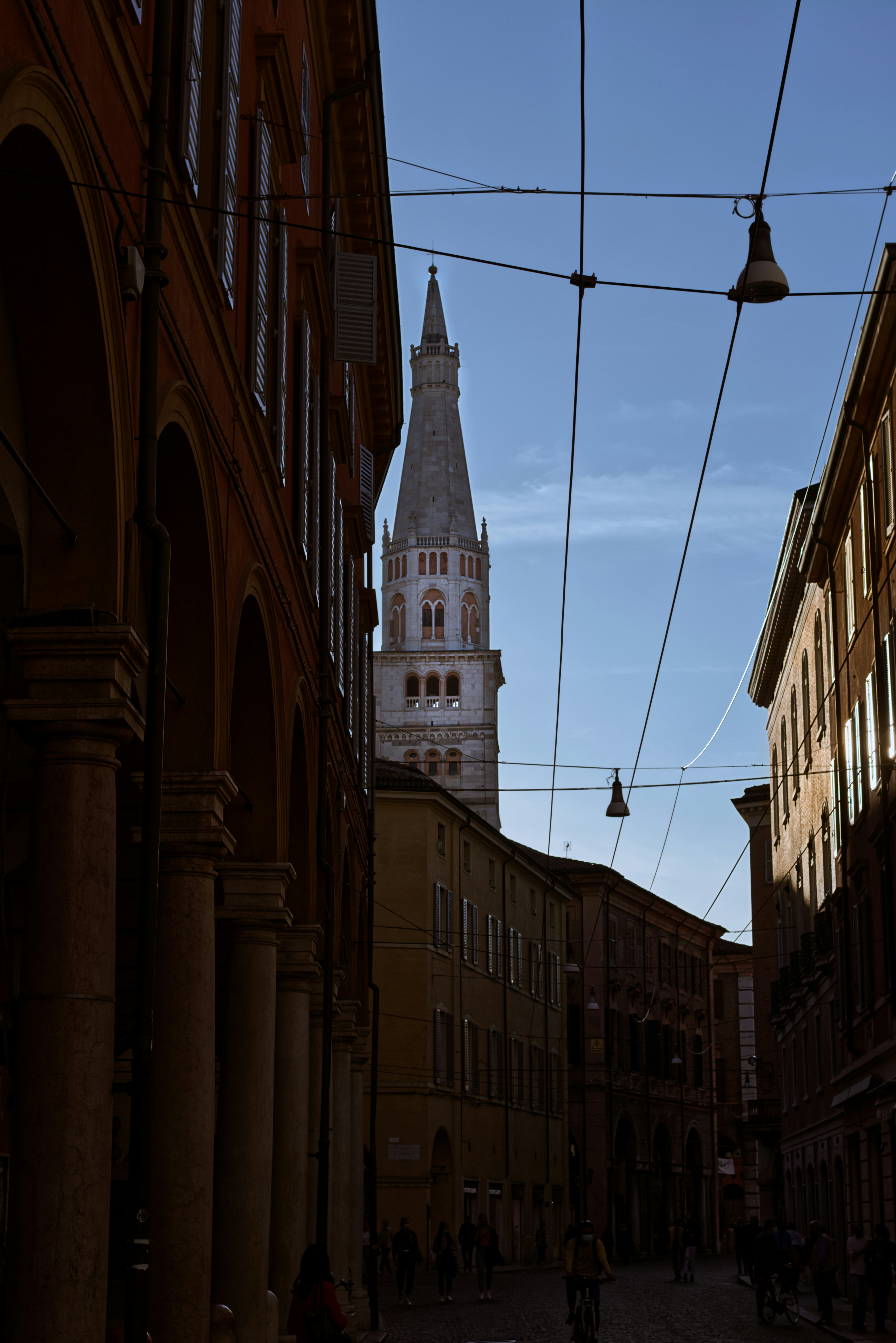 A narrow street framed by historic buildings, leading to a towering clock tower under a clear blue sky.
