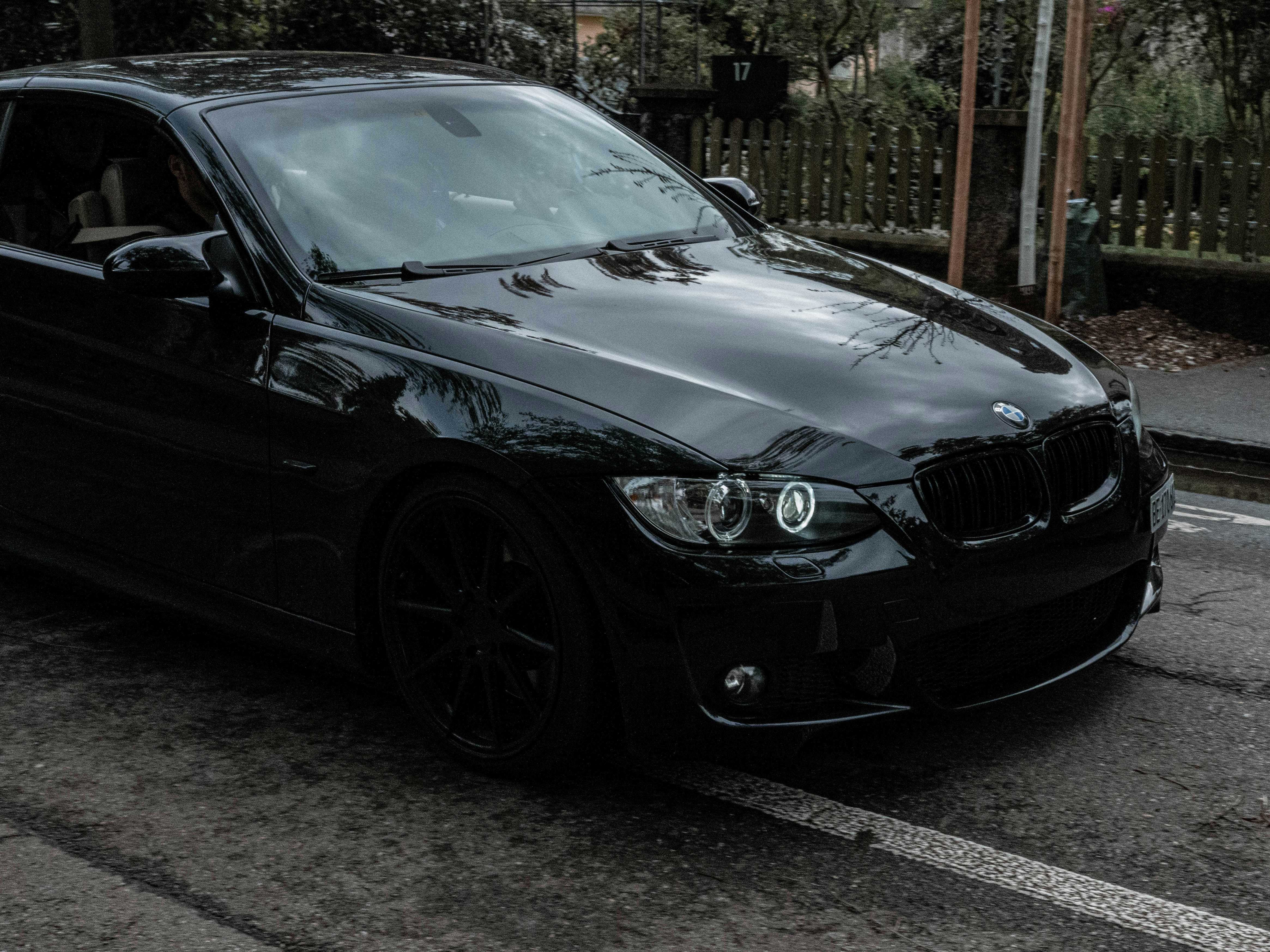 Sleek black BMW parked on a quiet street, showcasing its distinctive design and illuminated headlights.