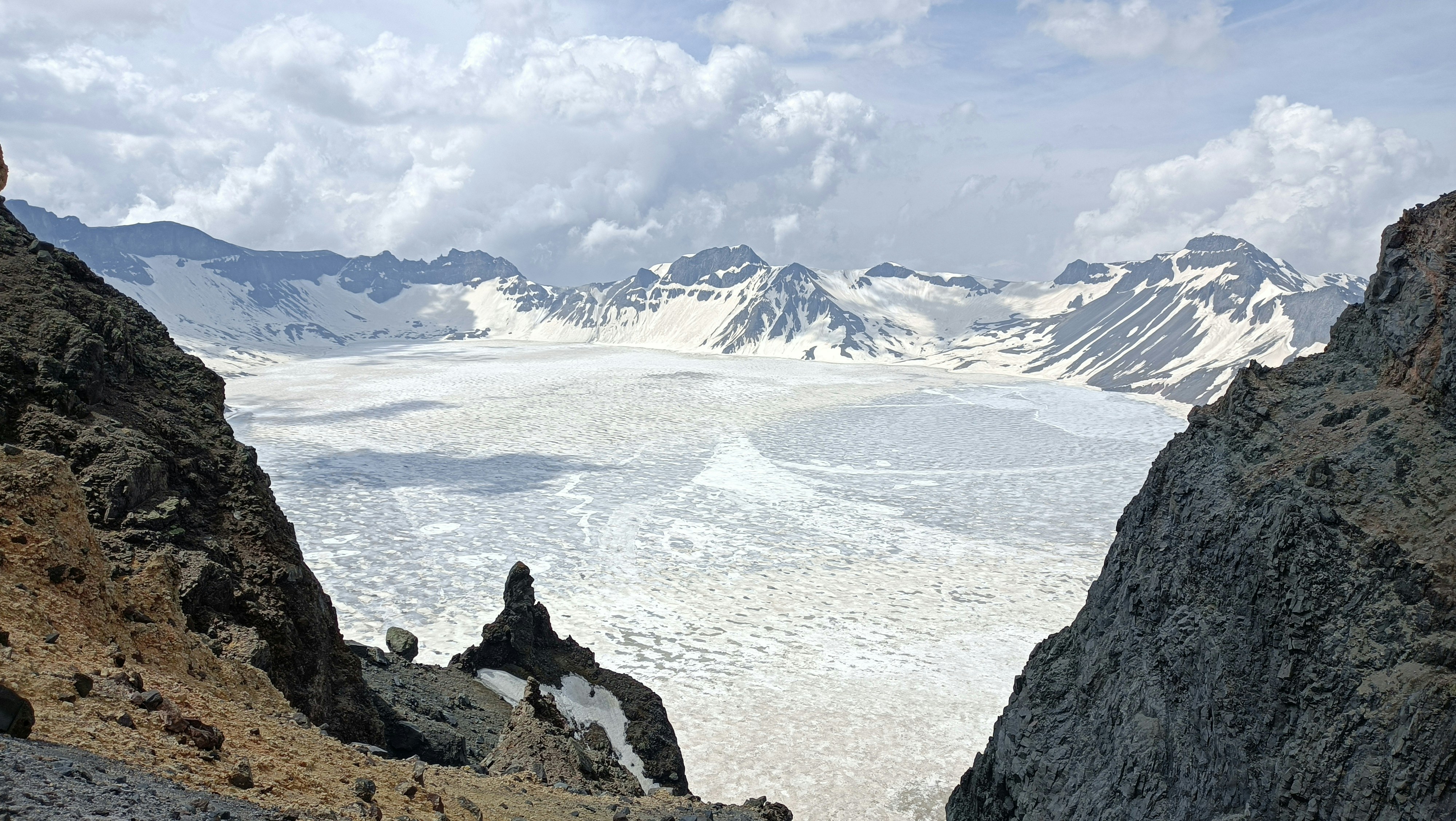 Rugged alpine landscape with a glacier-filled valley framed by dark cliff faces and distant snow-capped peaks.