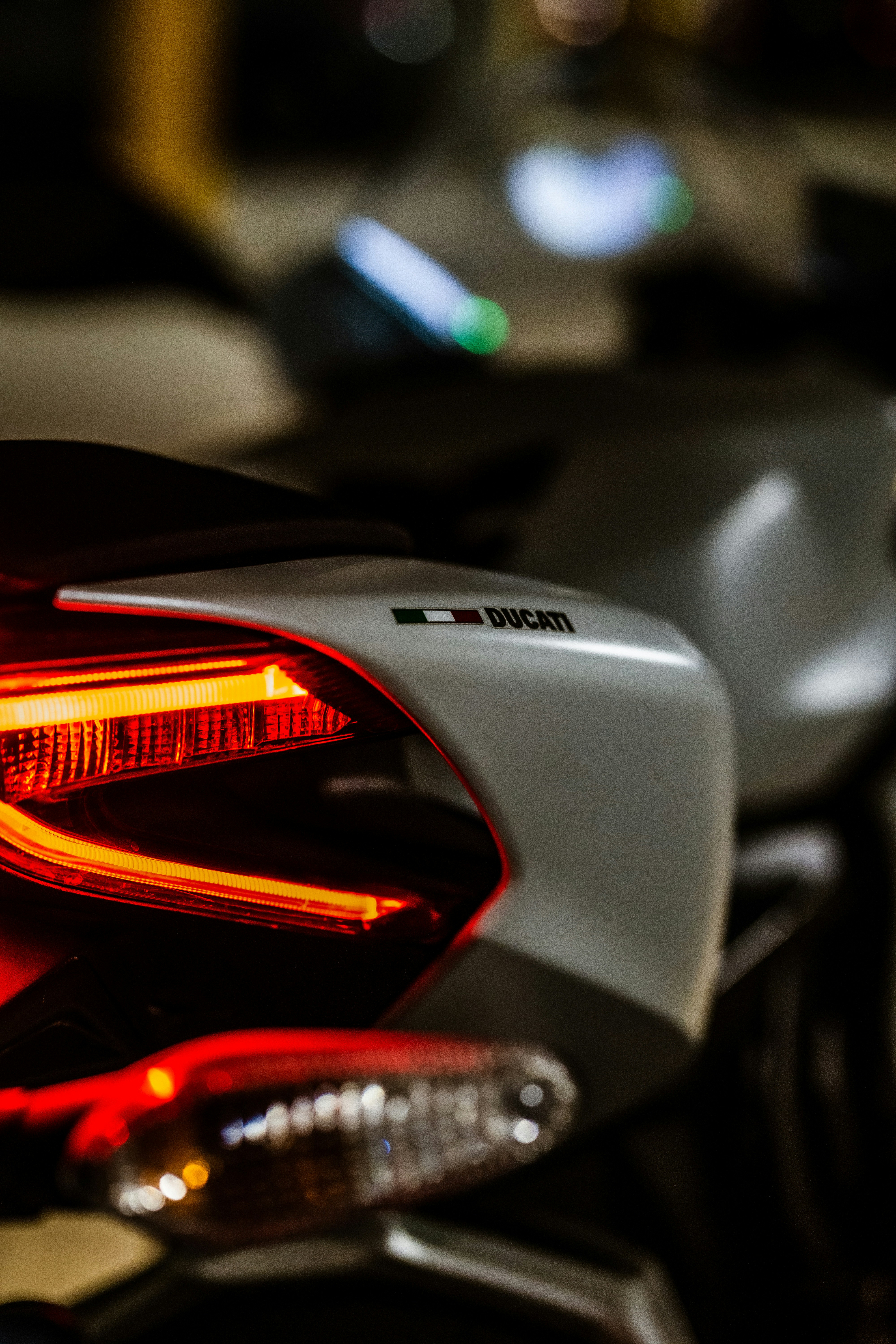 Close-up of a Ducati motorcycle's rear light and branding, showcasing intricate design and craftsmanship. The photo highlights the sleek lines and vibrant lighting.
