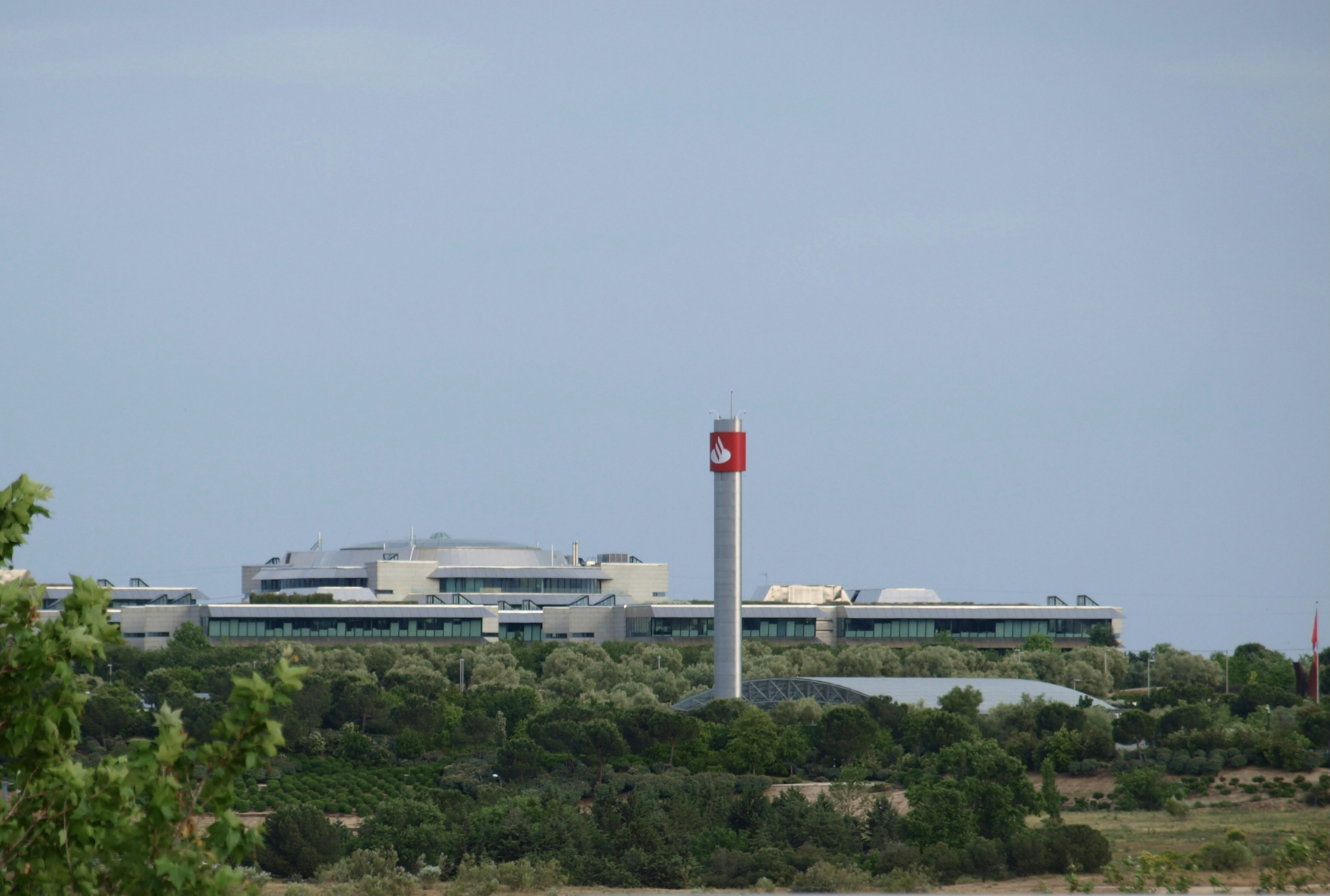 Contemporary building complex nestled among lush greenery, featuring a prominent red-topped tower.