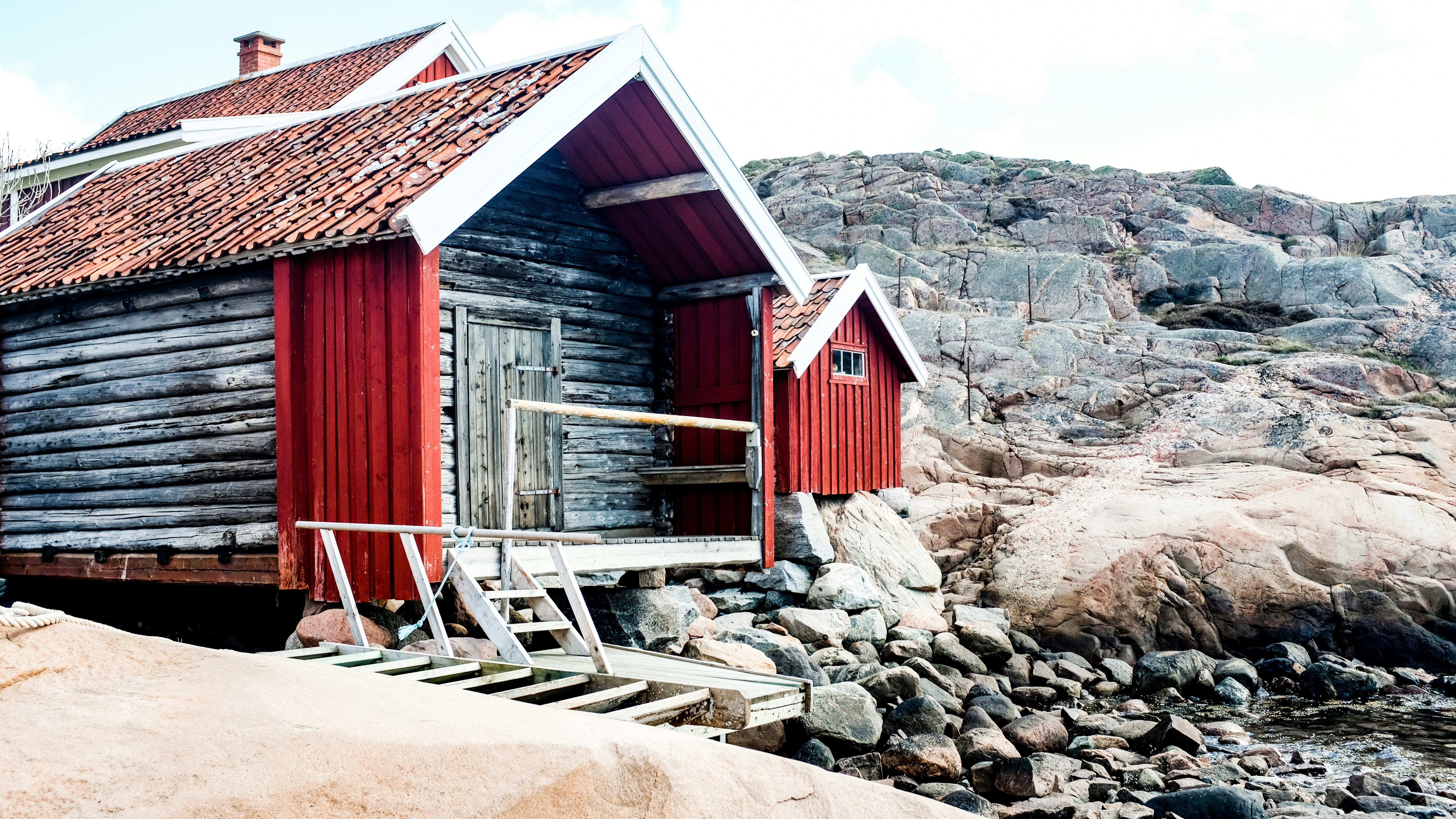 Weathered wooden cabins with red accents nestled against rocky terrain near the water's edge.