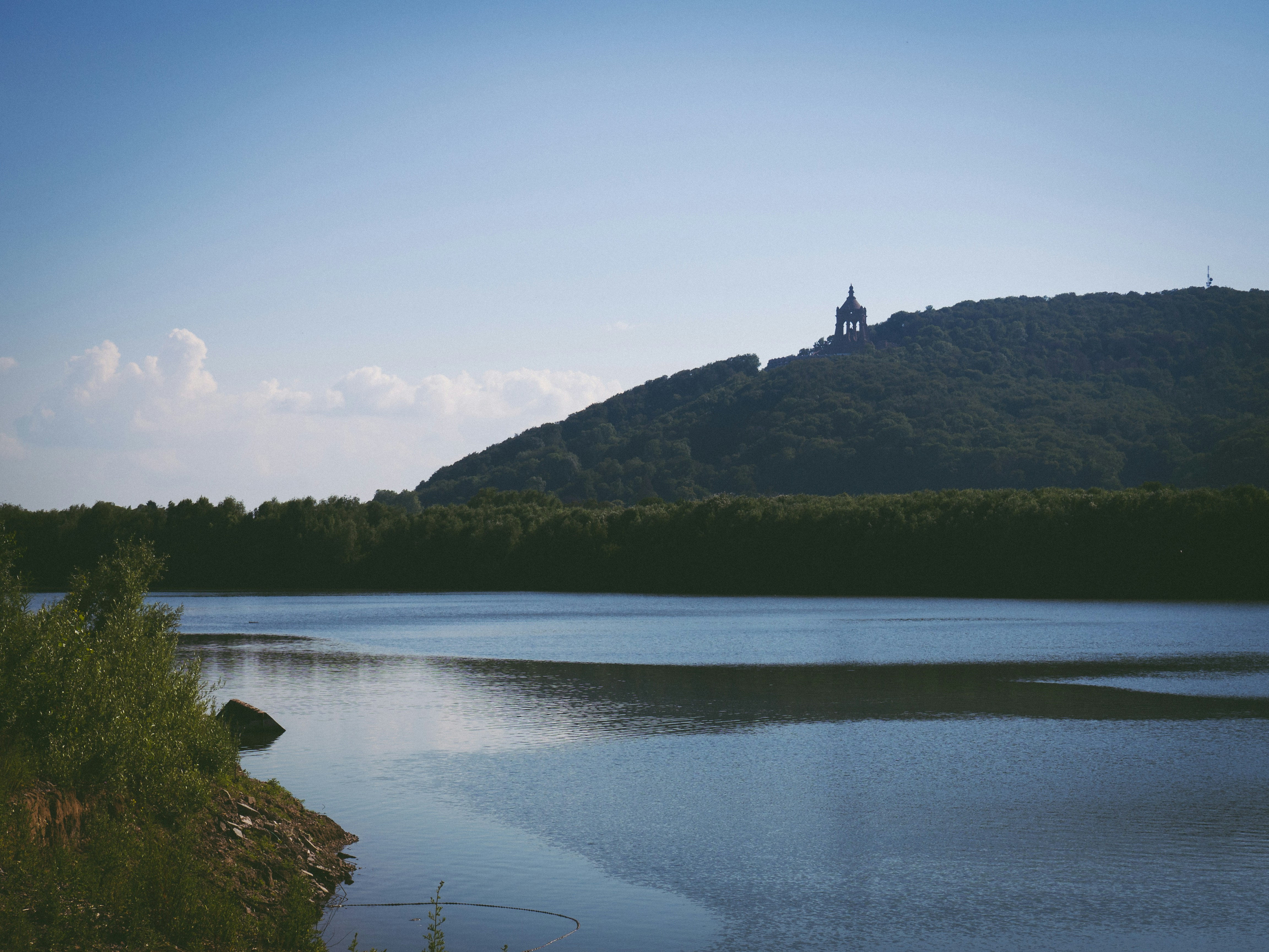A tranquil lakeside view with a distant hill crowned by a historical structure, reflecting the calmness of the water below.