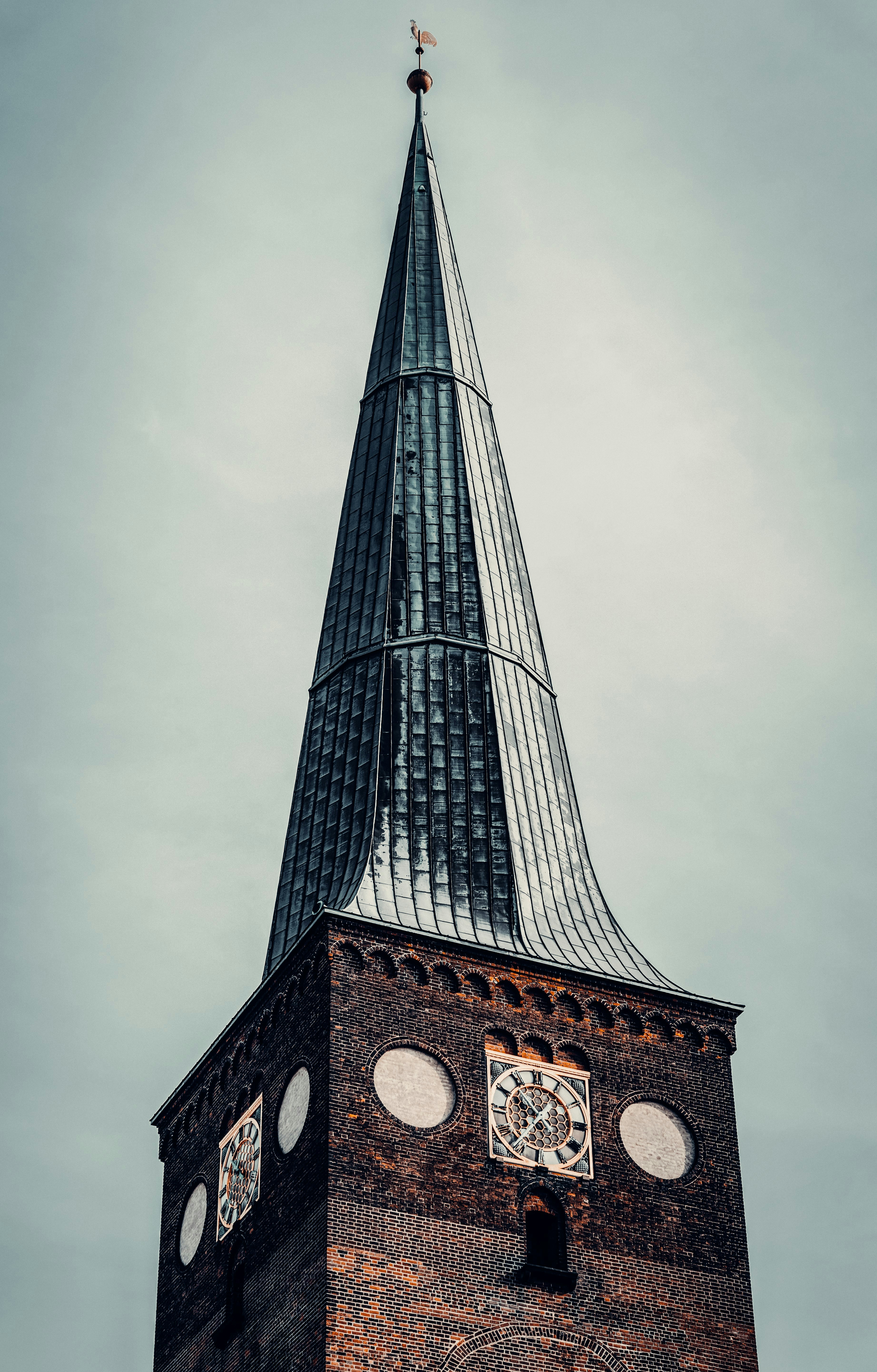 Tall church steeple with a distinctive pointed roof and clock faces, set against a muted sky.