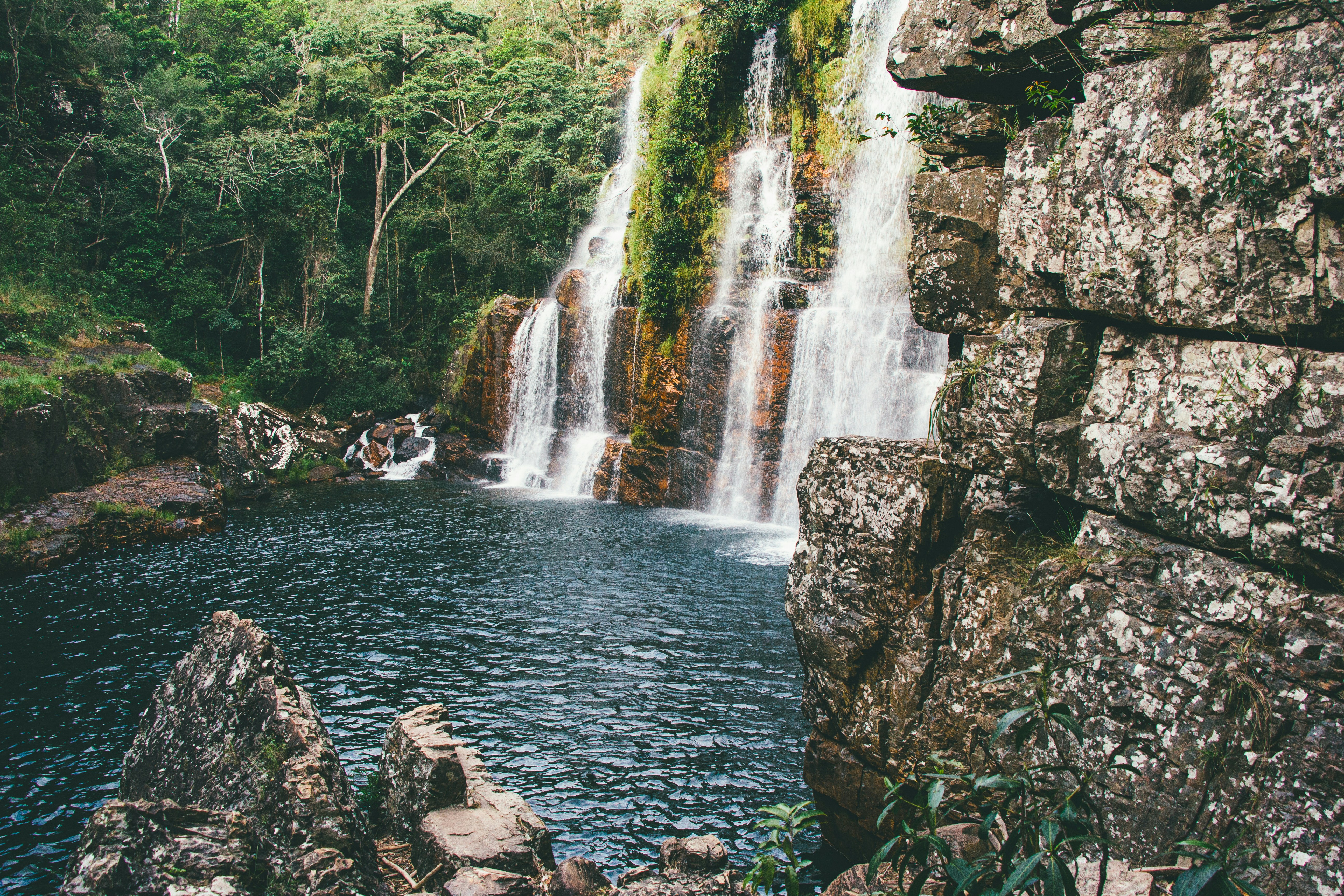 Waterfalls pouring over rocky cliffs into a serene pool surrounded by lush greenery.