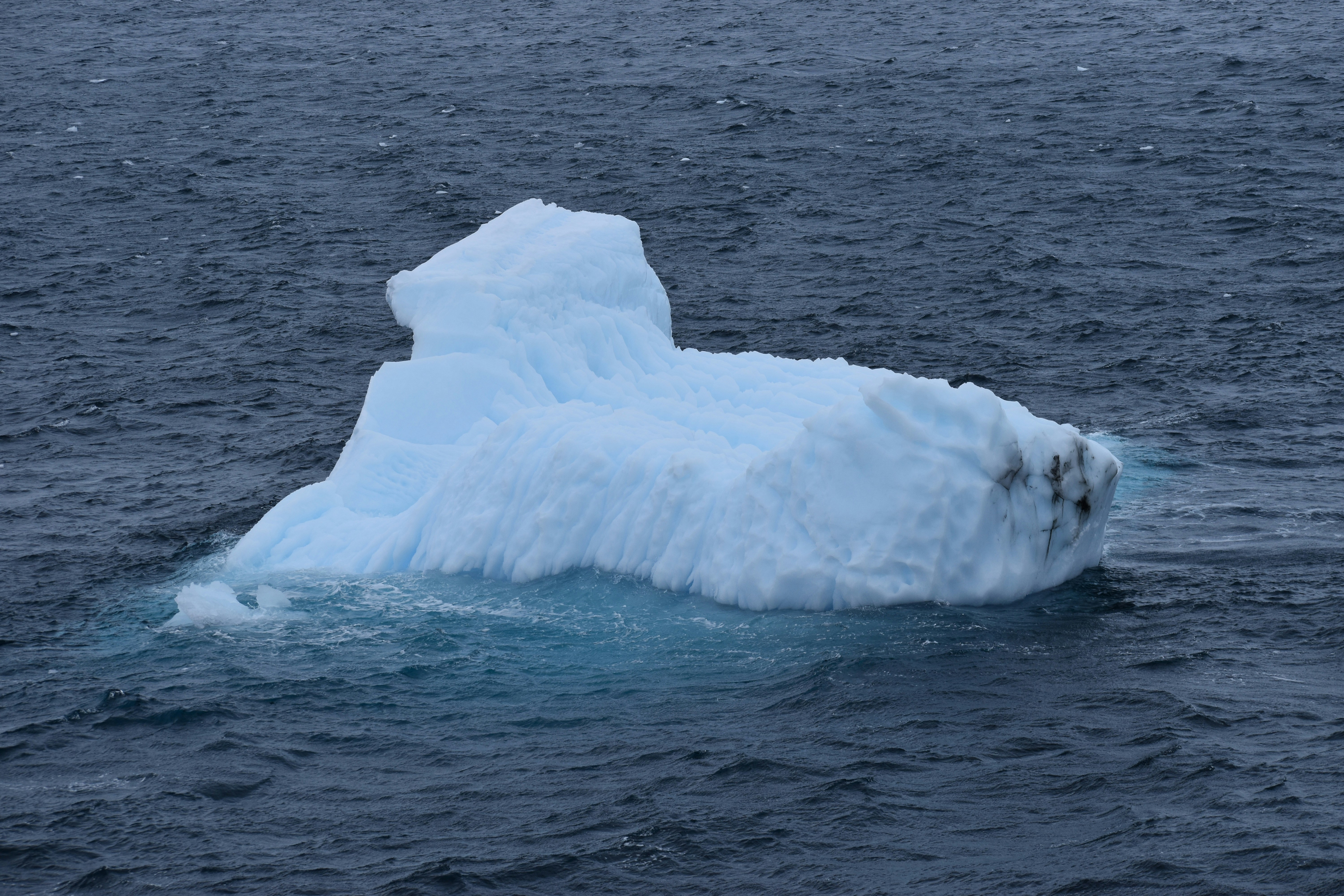 Lone iceberg floating in deep blue ocean waters, showcasing intricate textures and shades of white and blue. 