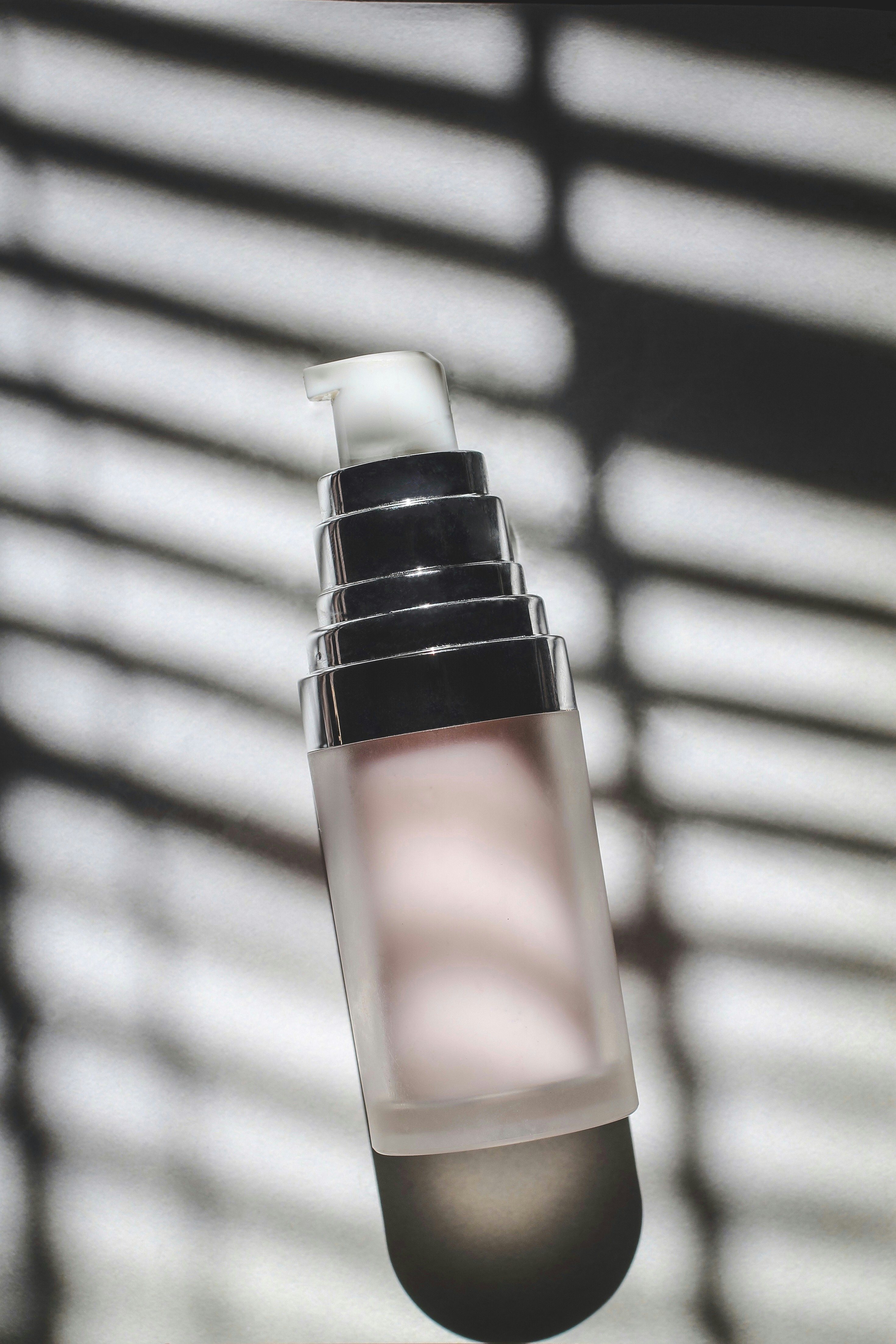 A sleek cosmetic serum bottle elegantly positioned, casting soft shadows across a textured surface.